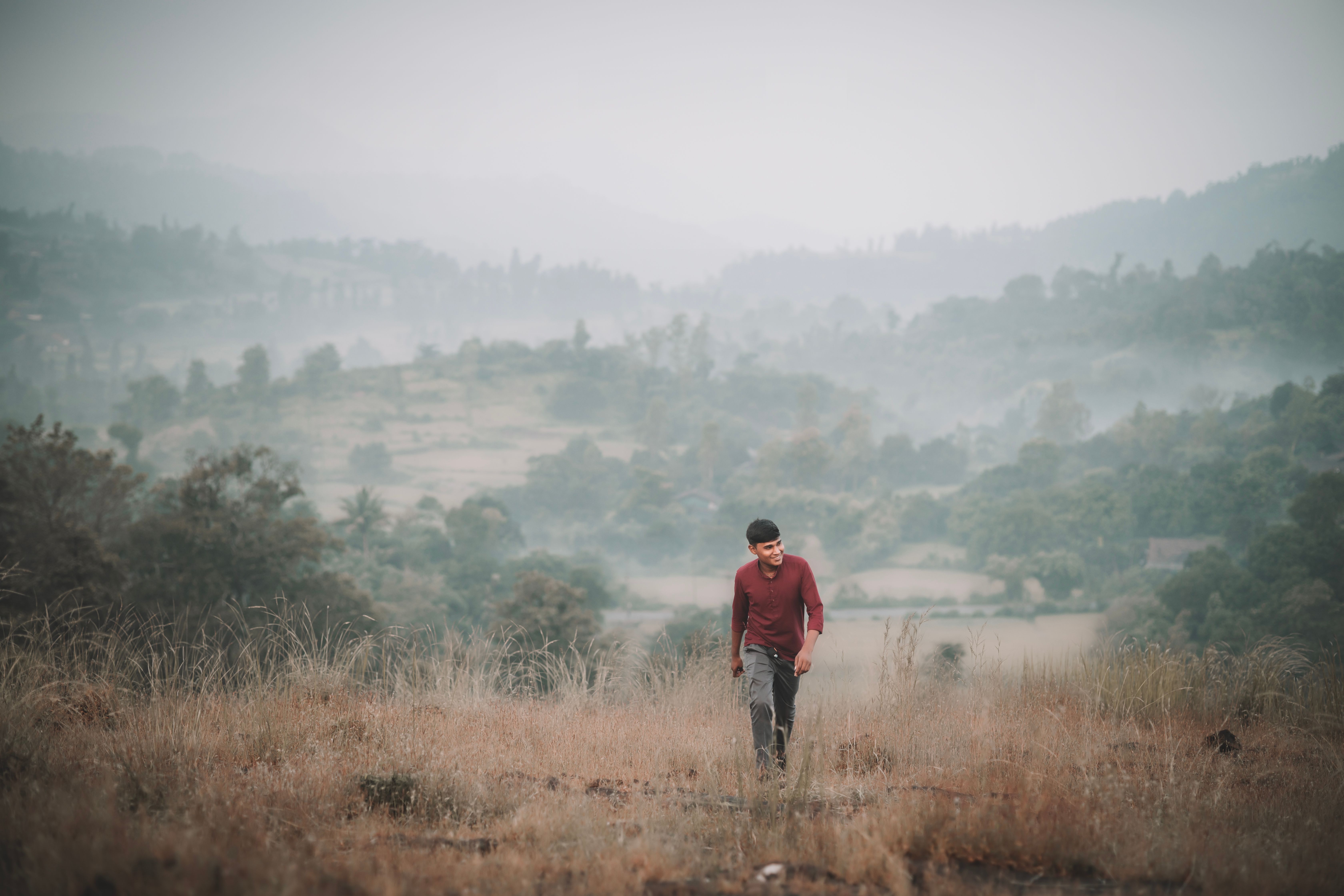Smiling Man Walking on Meadow against Hilly Landscape in Fog · Free ...