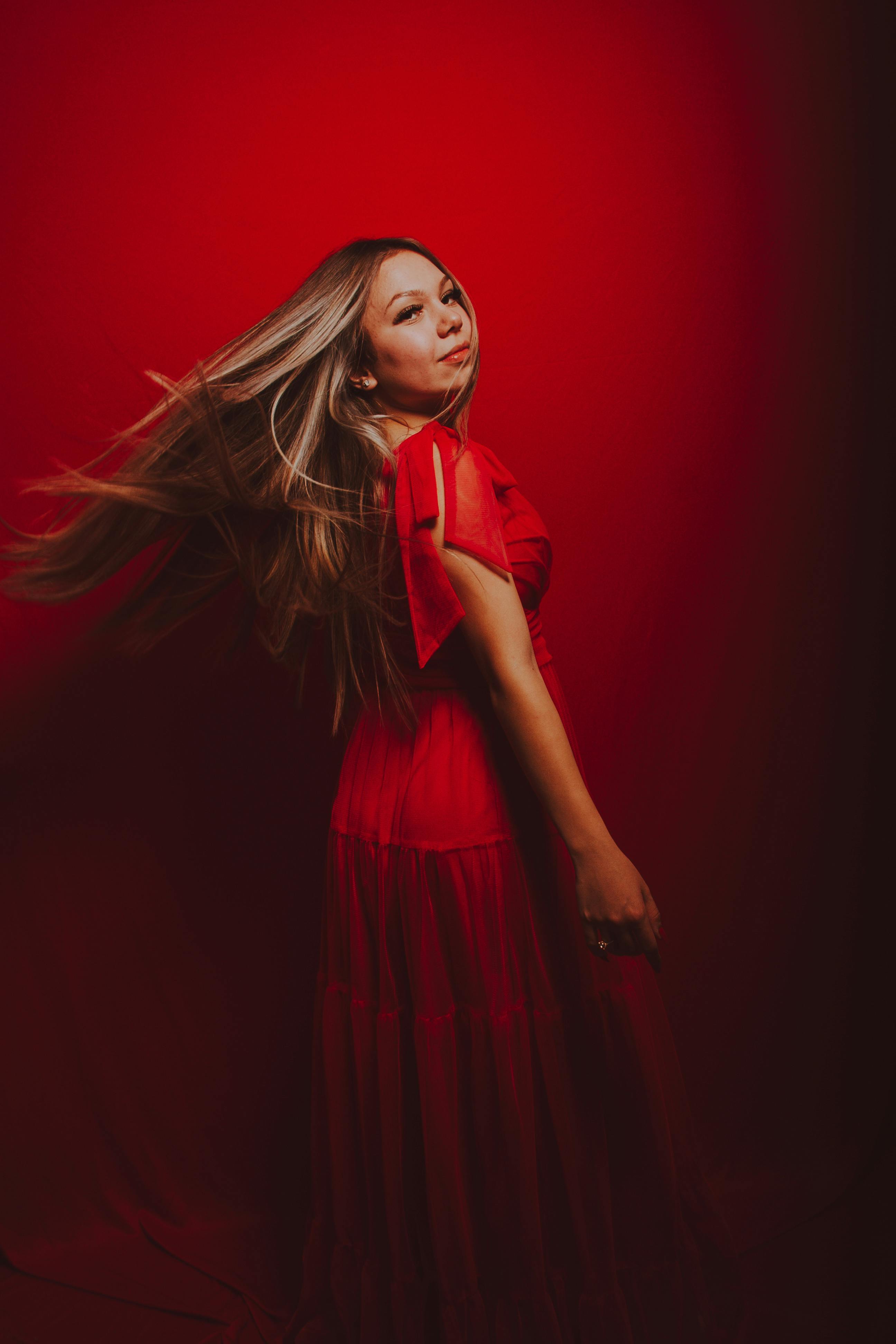 Young Woman in a Red Dress Posing on Red Background · Free Stock Photo
