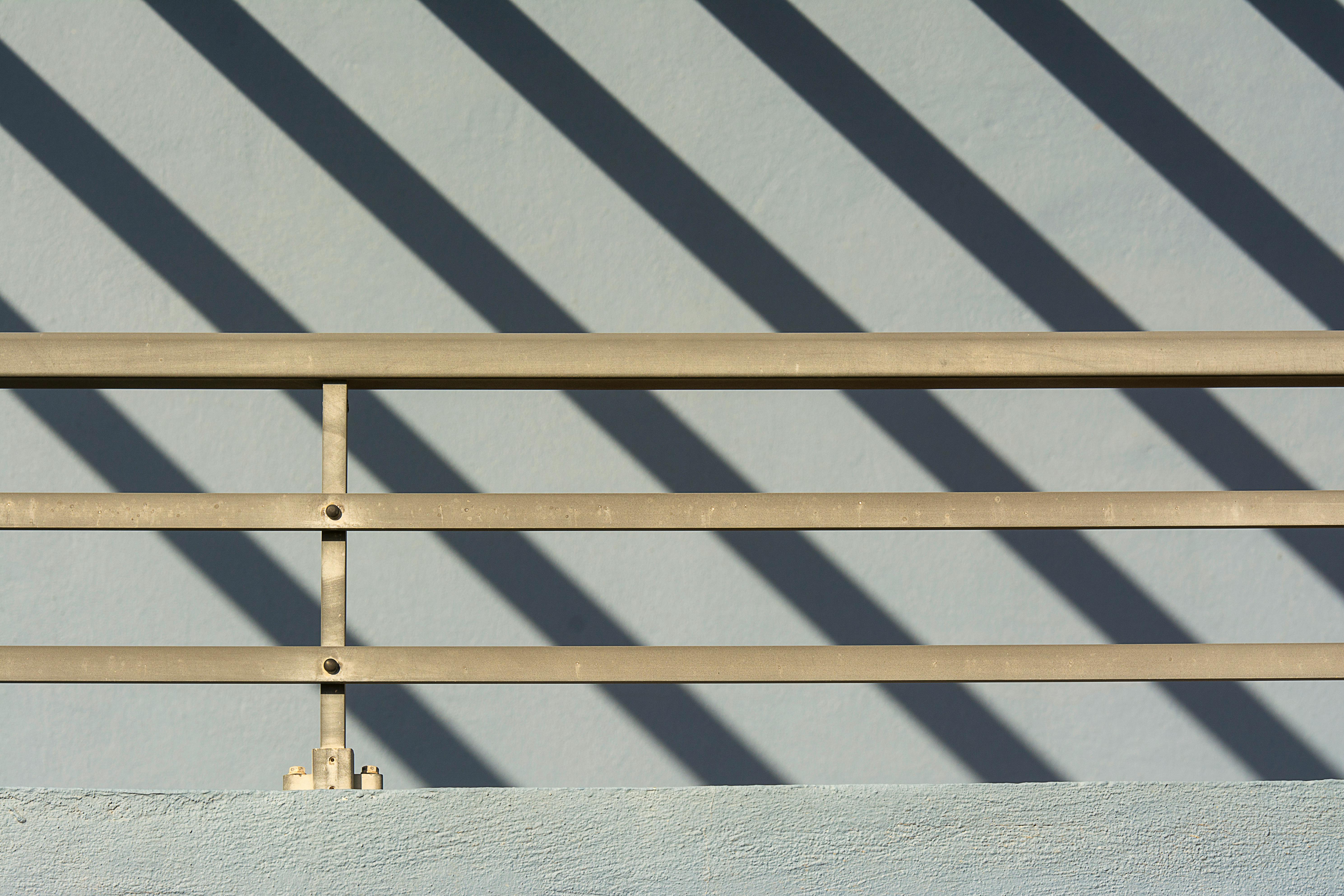 A railing with shadows on it against a blue wall · Free Stock Photo