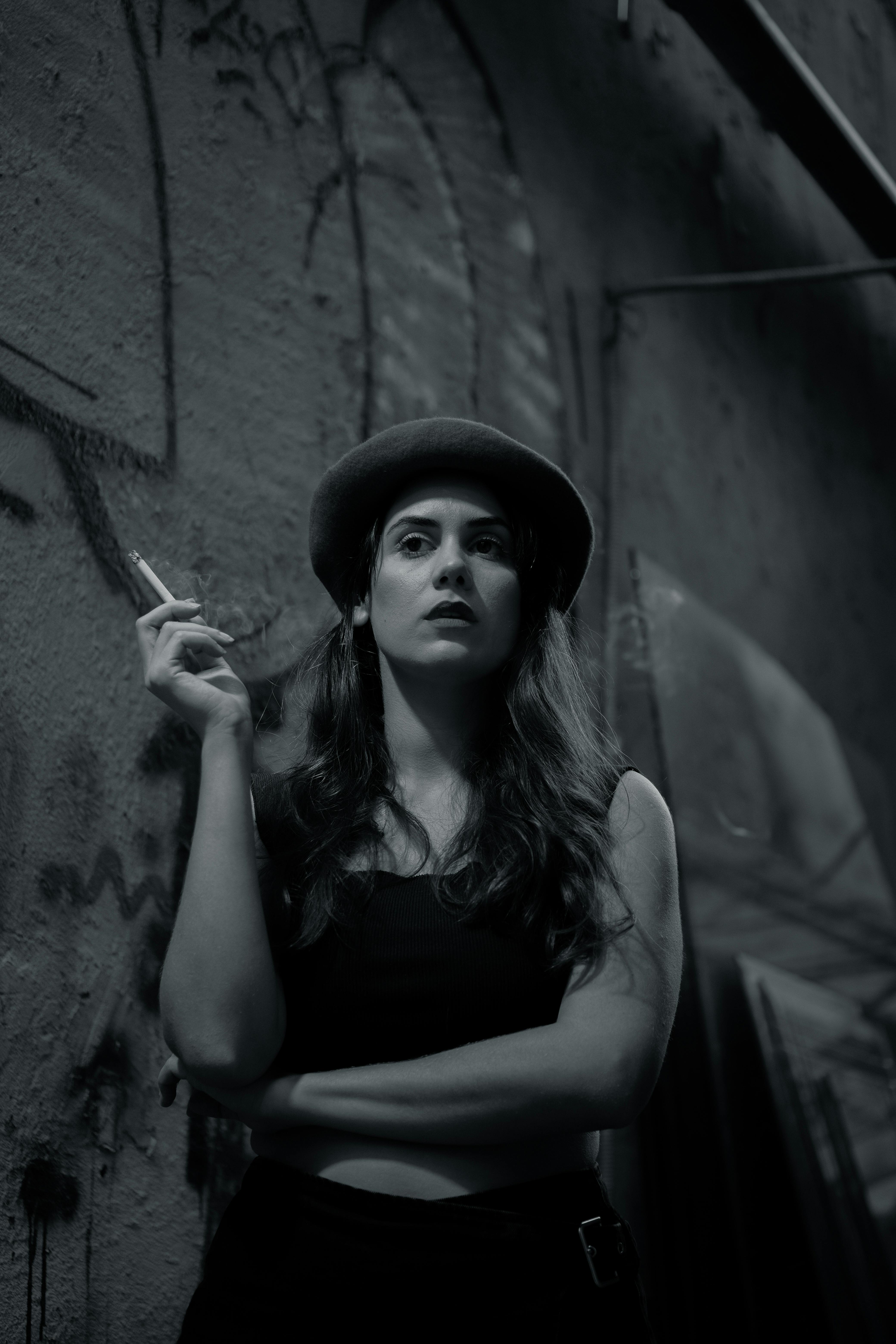 Woman in a Hat and Crop Top Smoking a Cigarette in the Back Alley ...