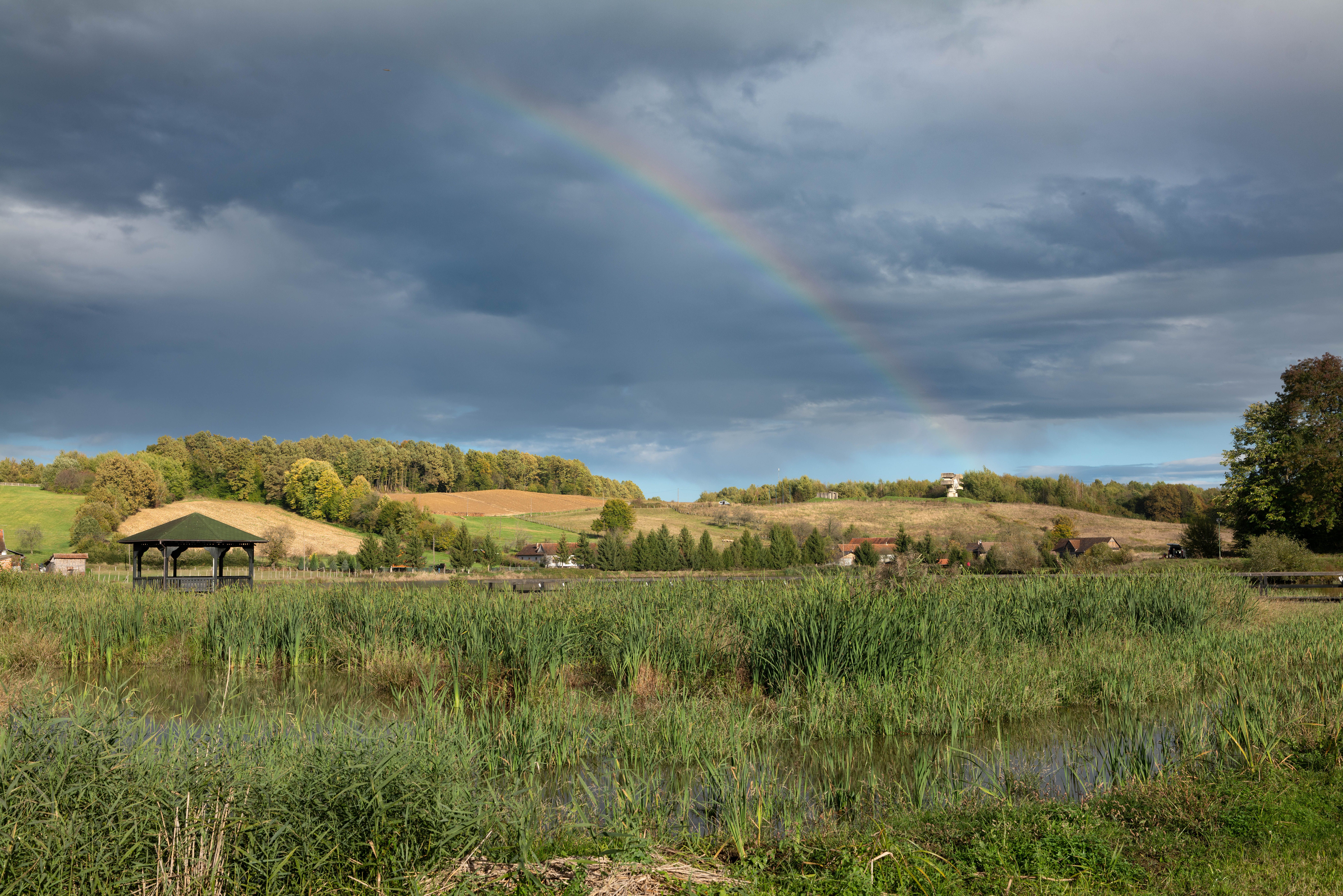 A rainbow appears over a field with a barn · Free Stock Photo