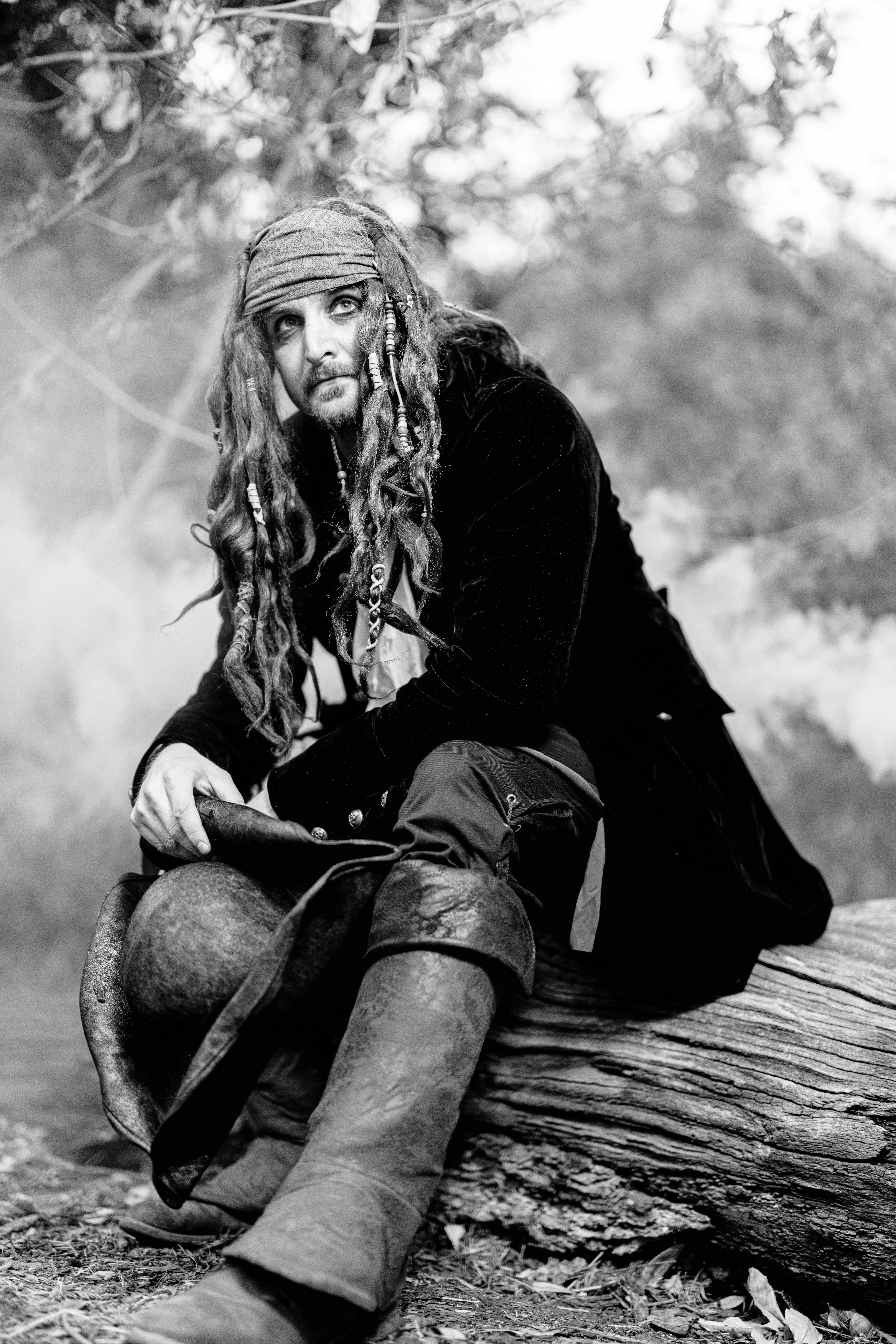 Grayscale Shot of a Man Dressed as a Pirate Sitting on a Fallen Tree ...