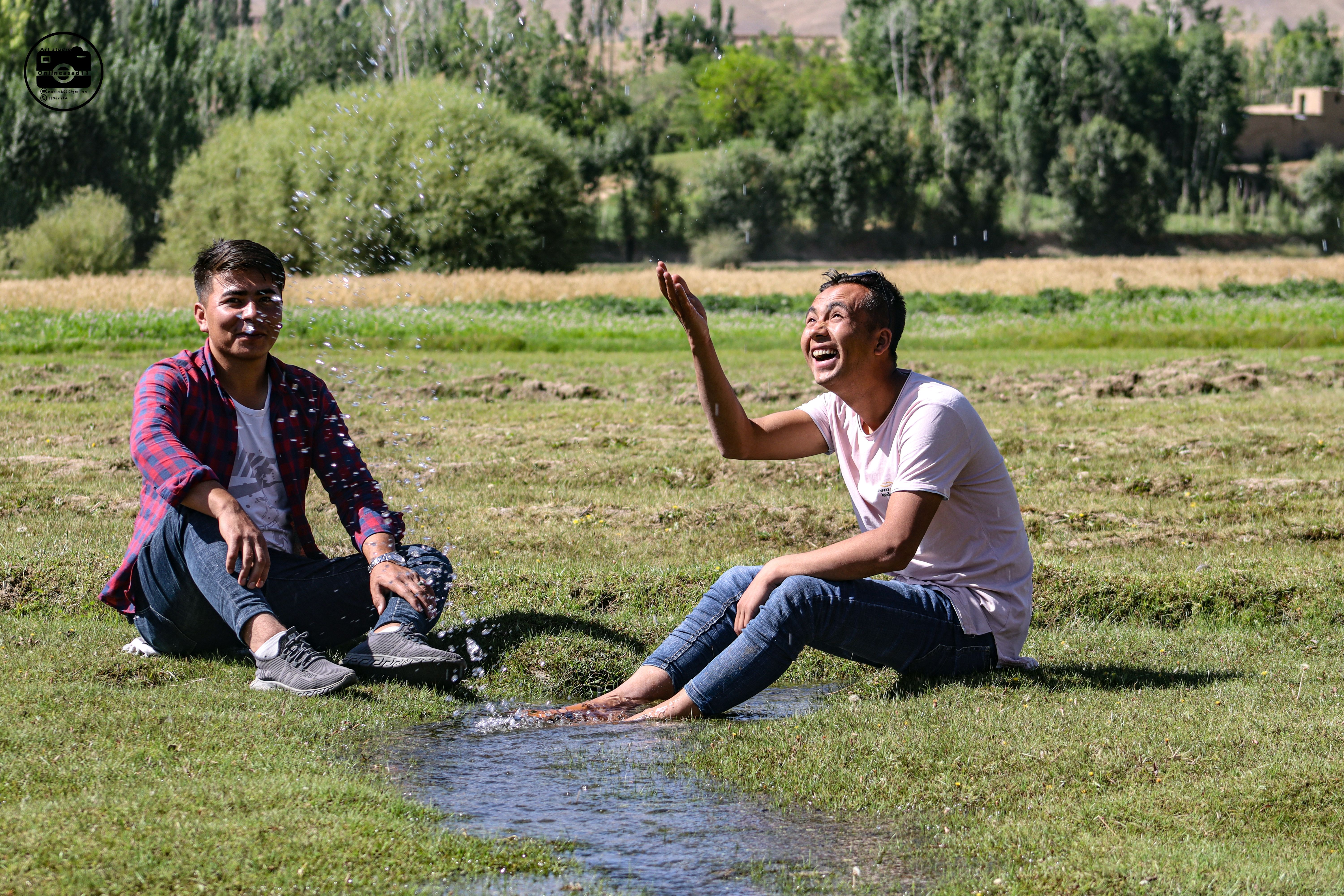 Smiling Men Sitting on Ground and Splashing Water · Free Stock Photo