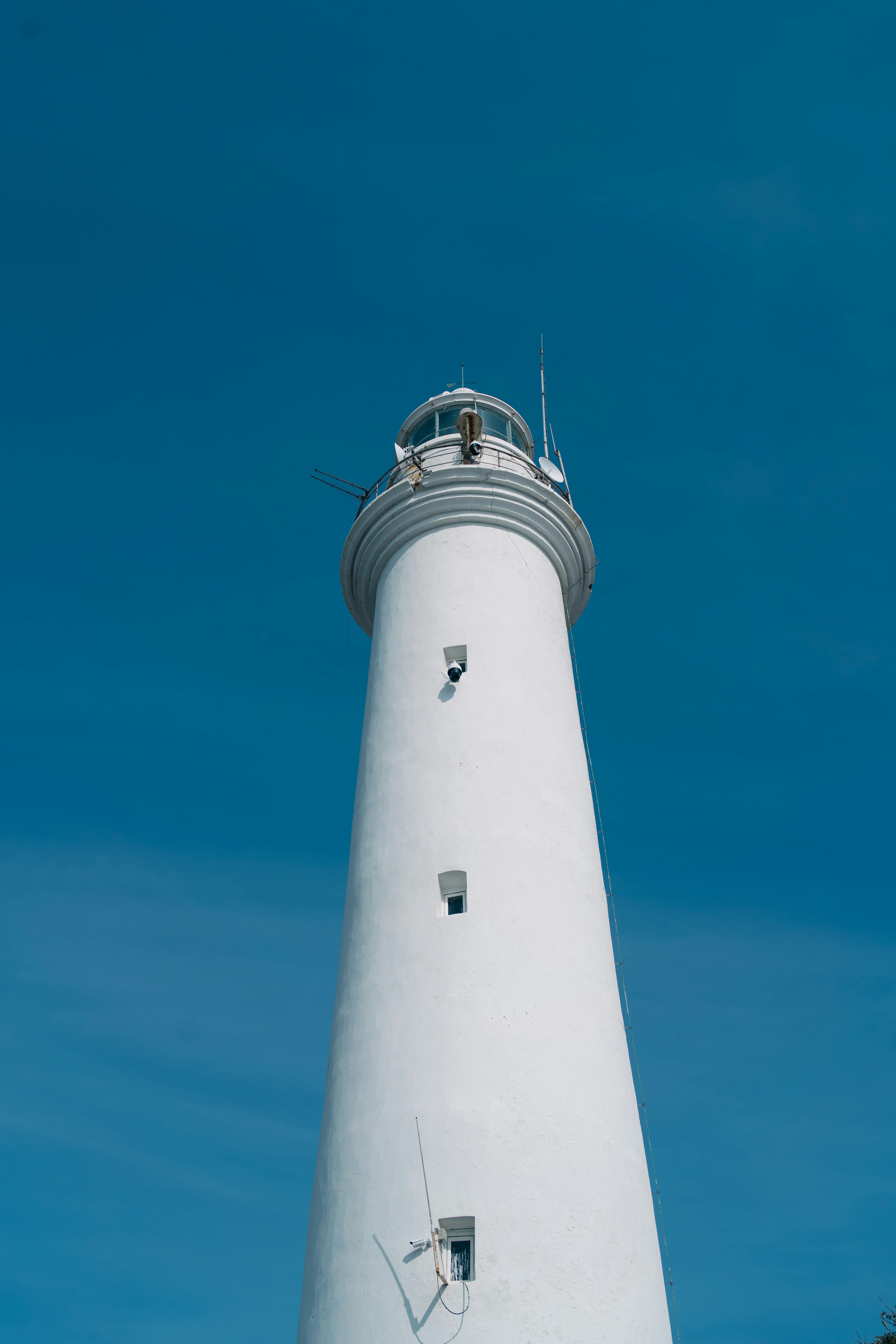 White Lighthouse Tower Beside Concrete Buildings · Free Stock Photo
