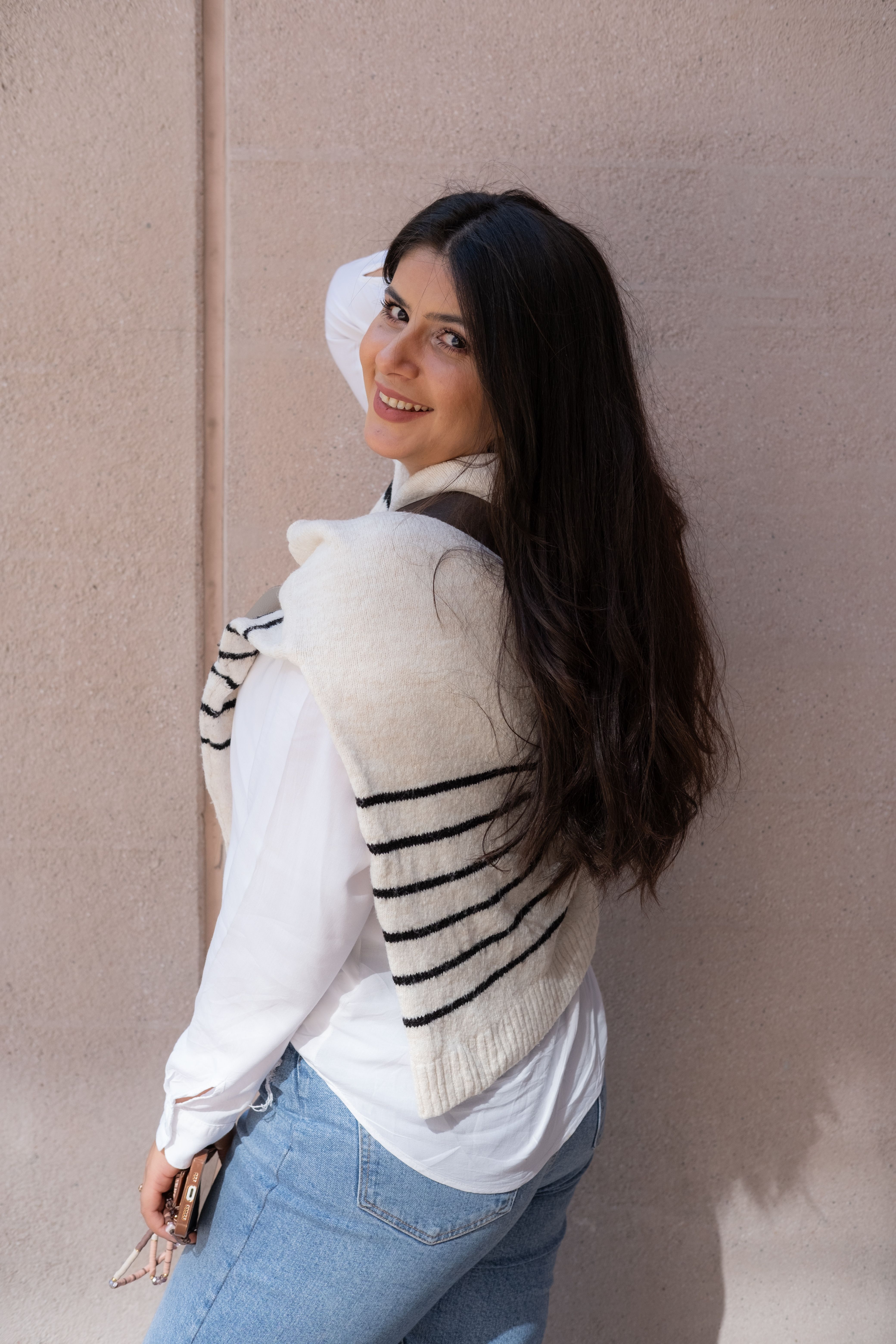 Smiling Woman Posing in a White Blouse with a Striped Sweater Draped ...