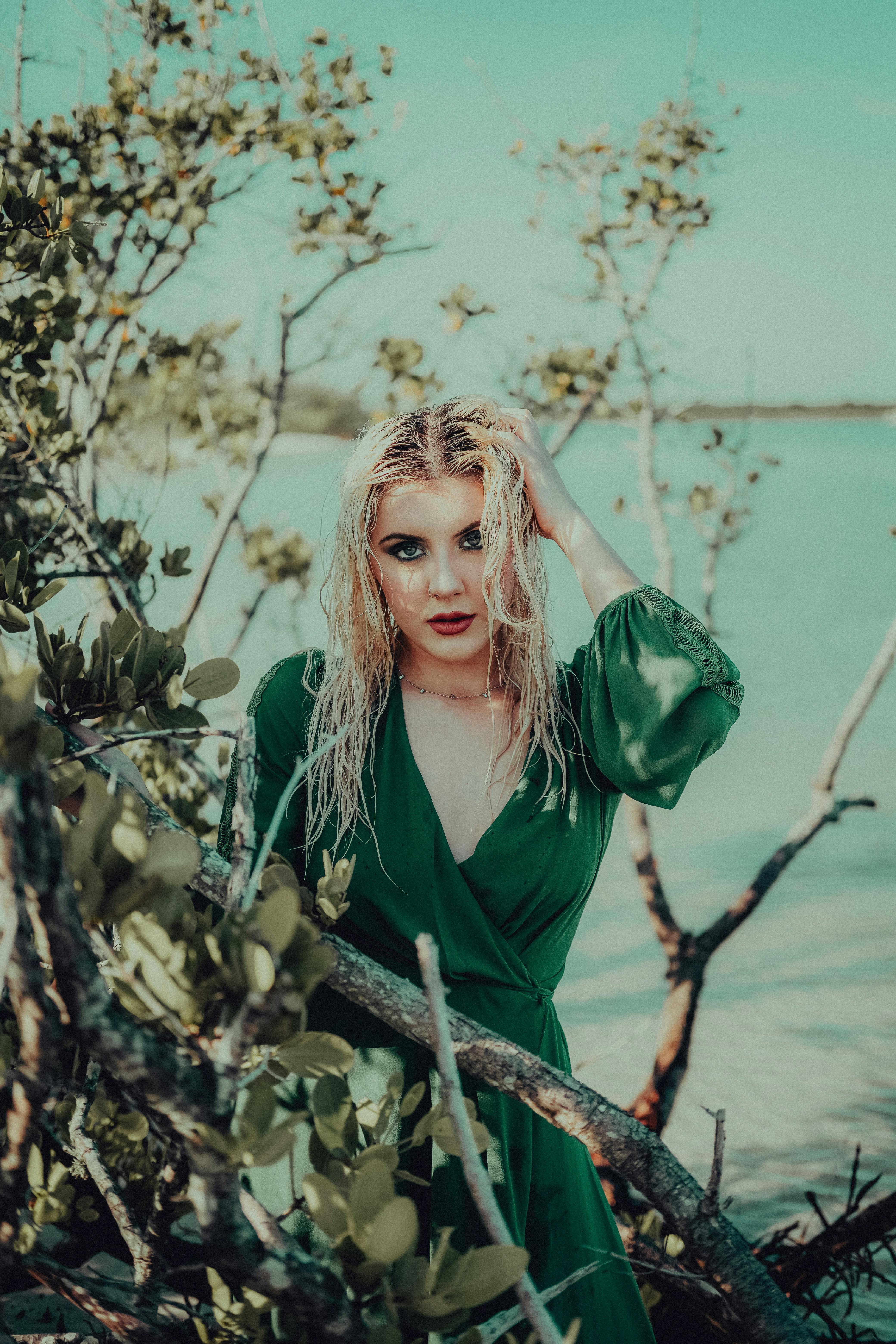 Fixing Hair Blonde Woman in Green Dress in Shrub by Sea · Free Stock Photo