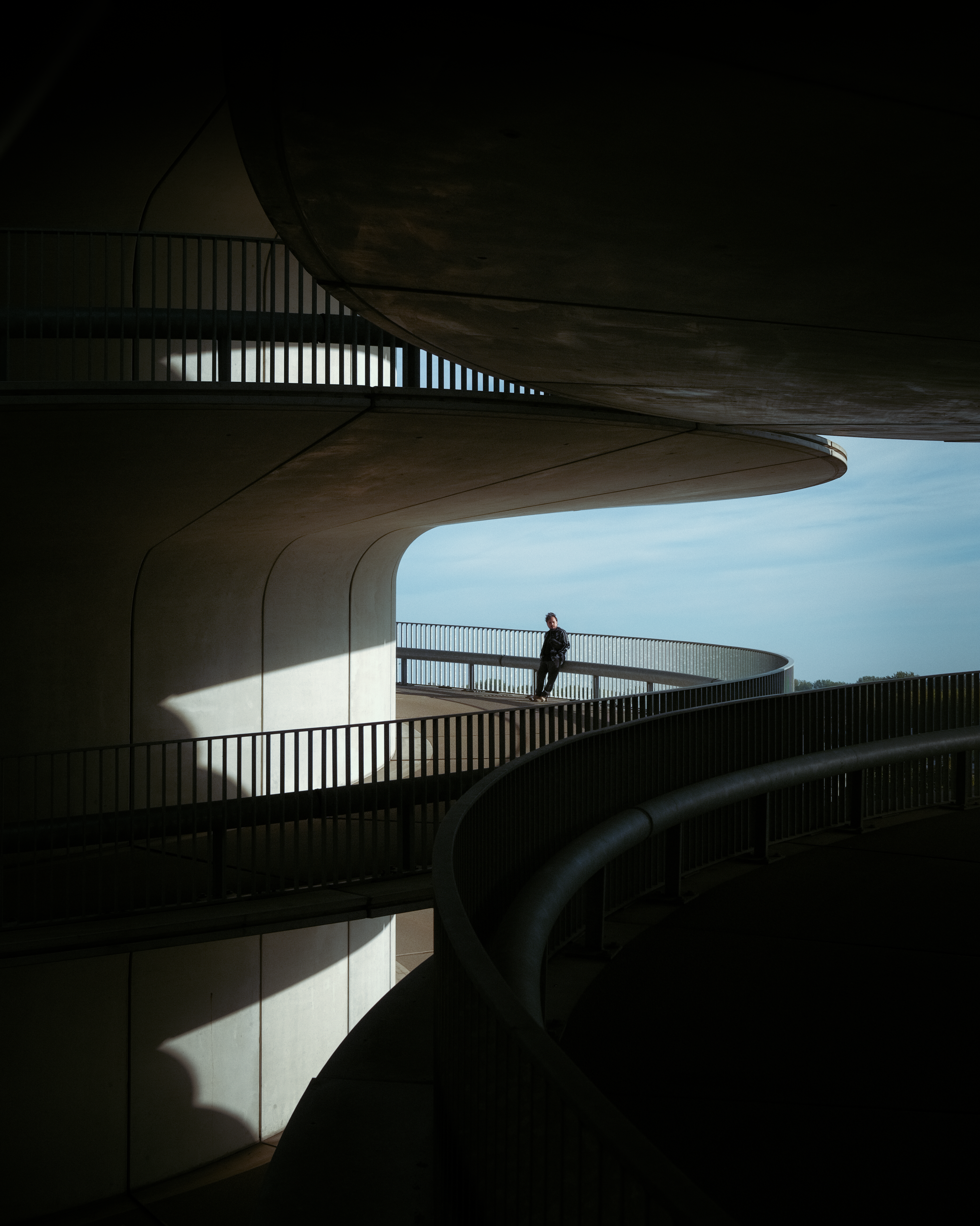 Man Leaning on a Railing of a Spiral Parking Lot Road · Free Stock Photo