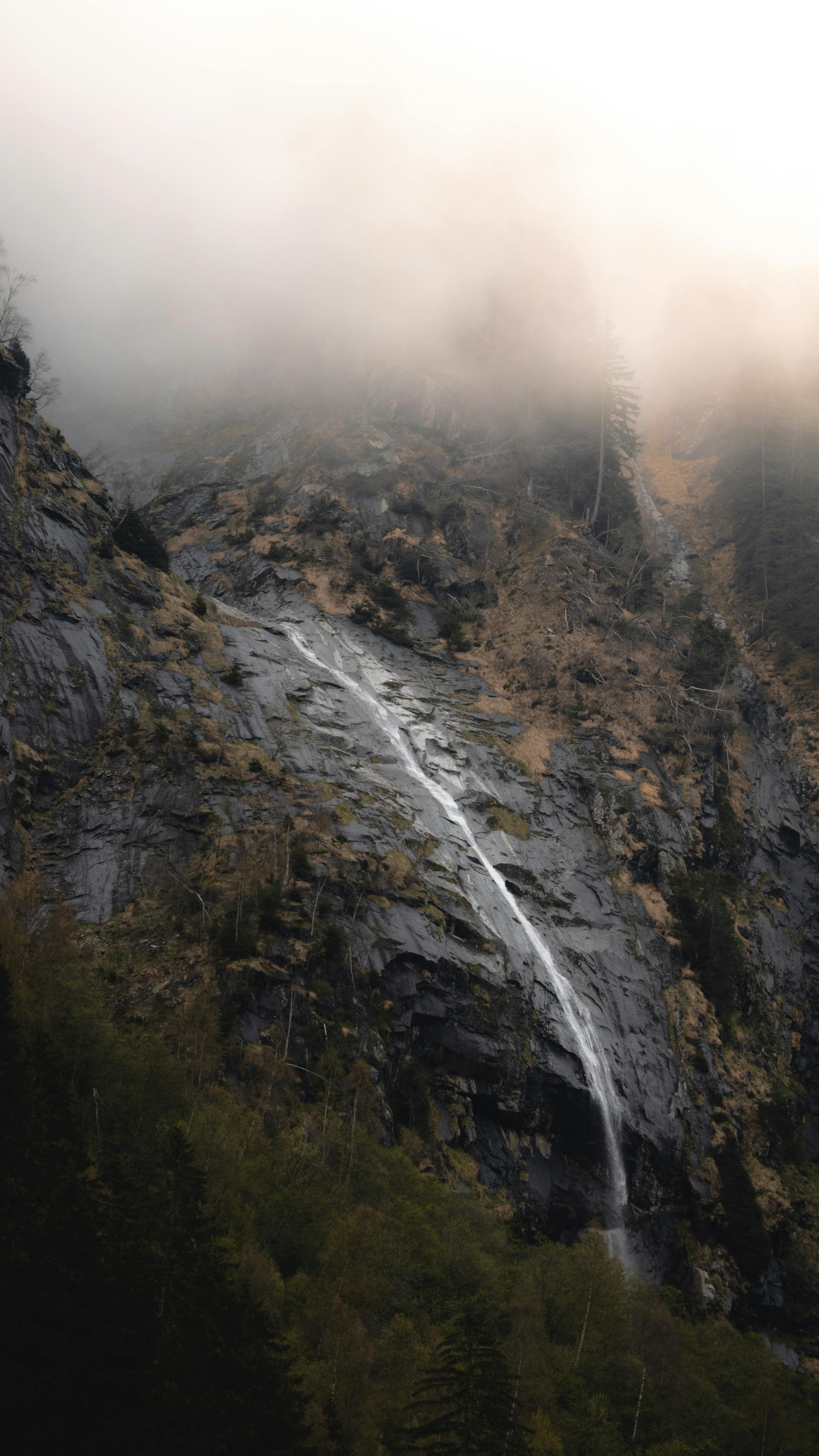 A waterfall is seen in the foggy mountains · Free Stock Photo