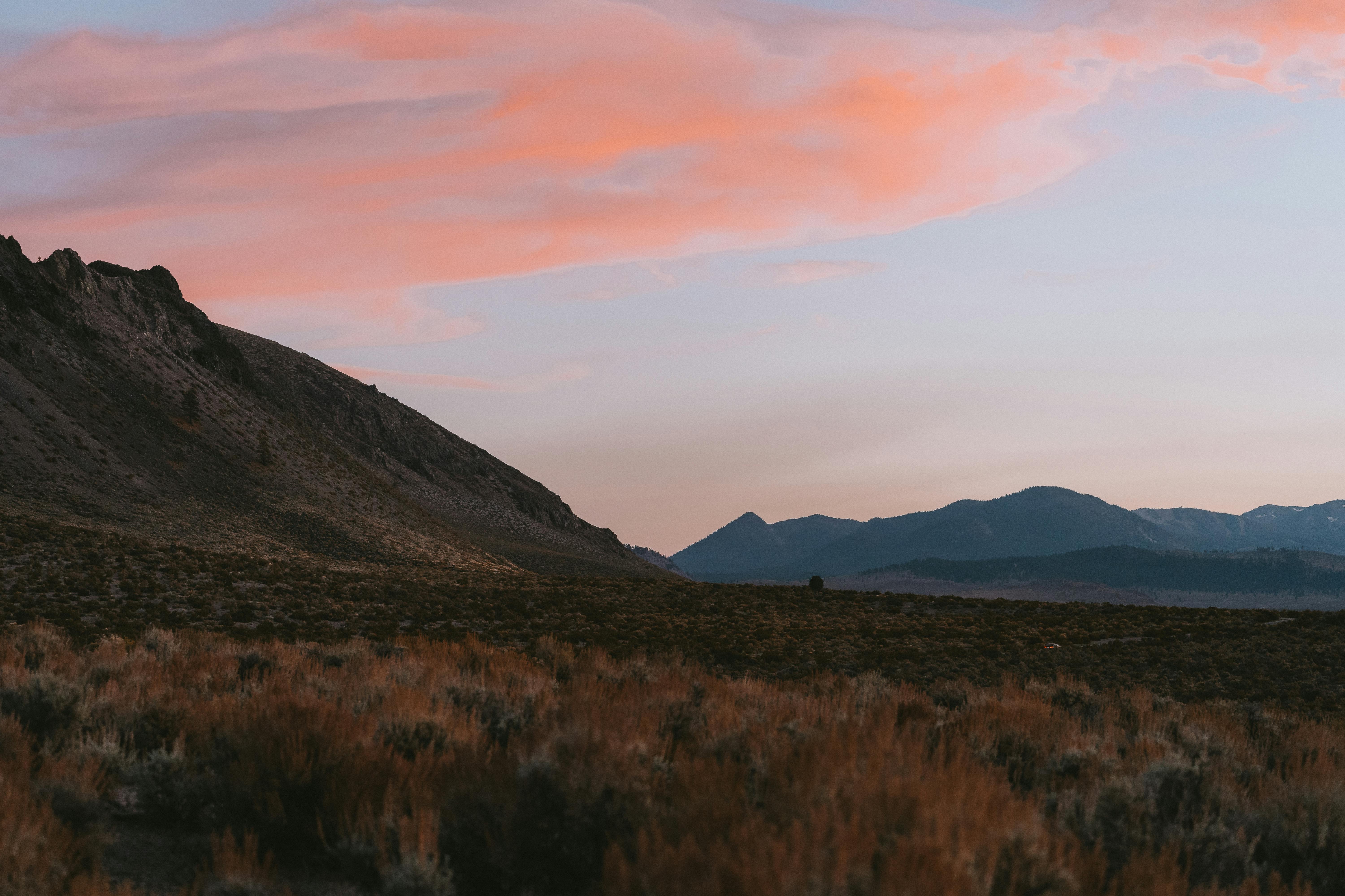 Scenic View of a Grass Field and Mountains at Sunset · Free Stock Photo