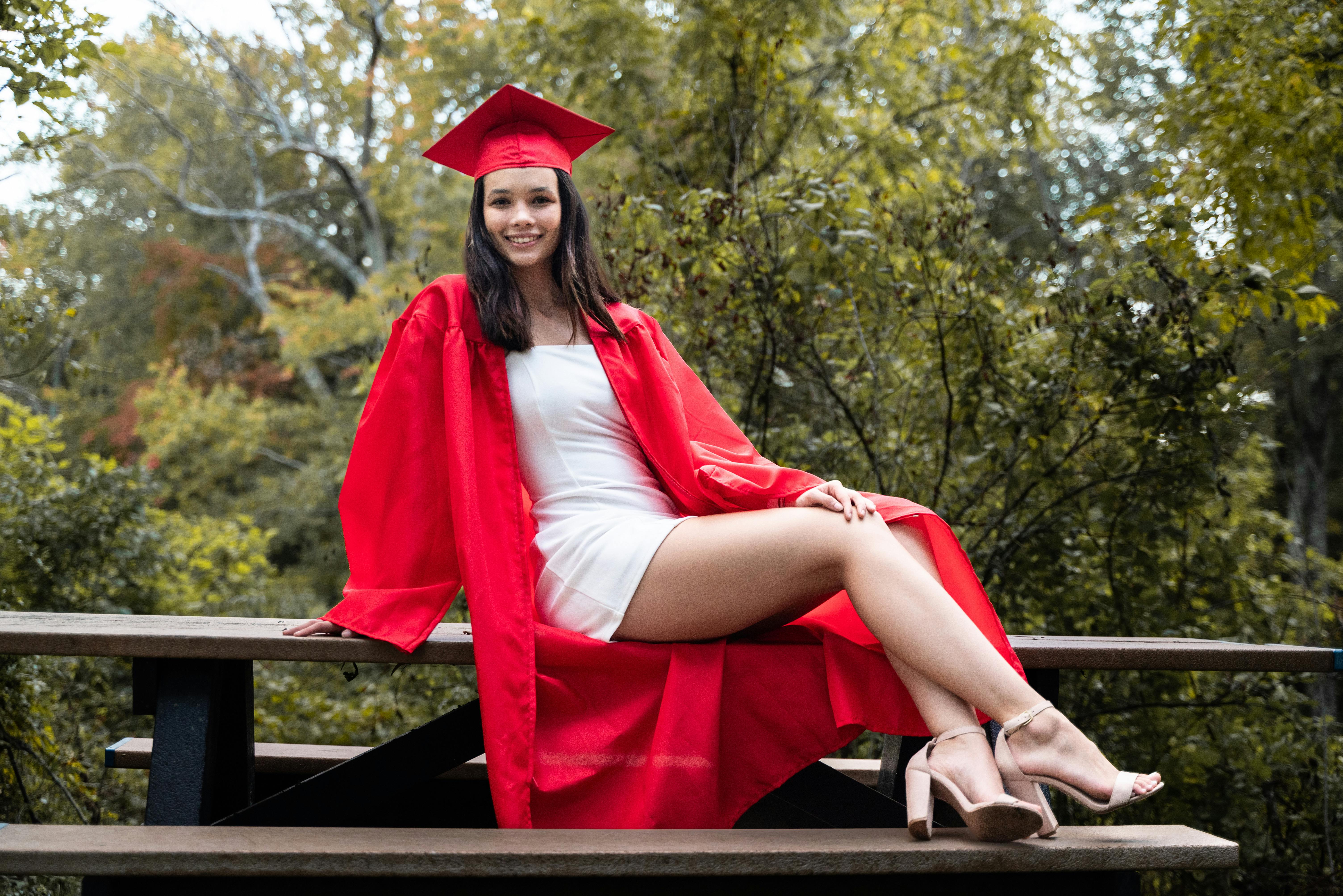 Smiling Graduate in Red Gown and Academic Hat Sitting on Table and ...