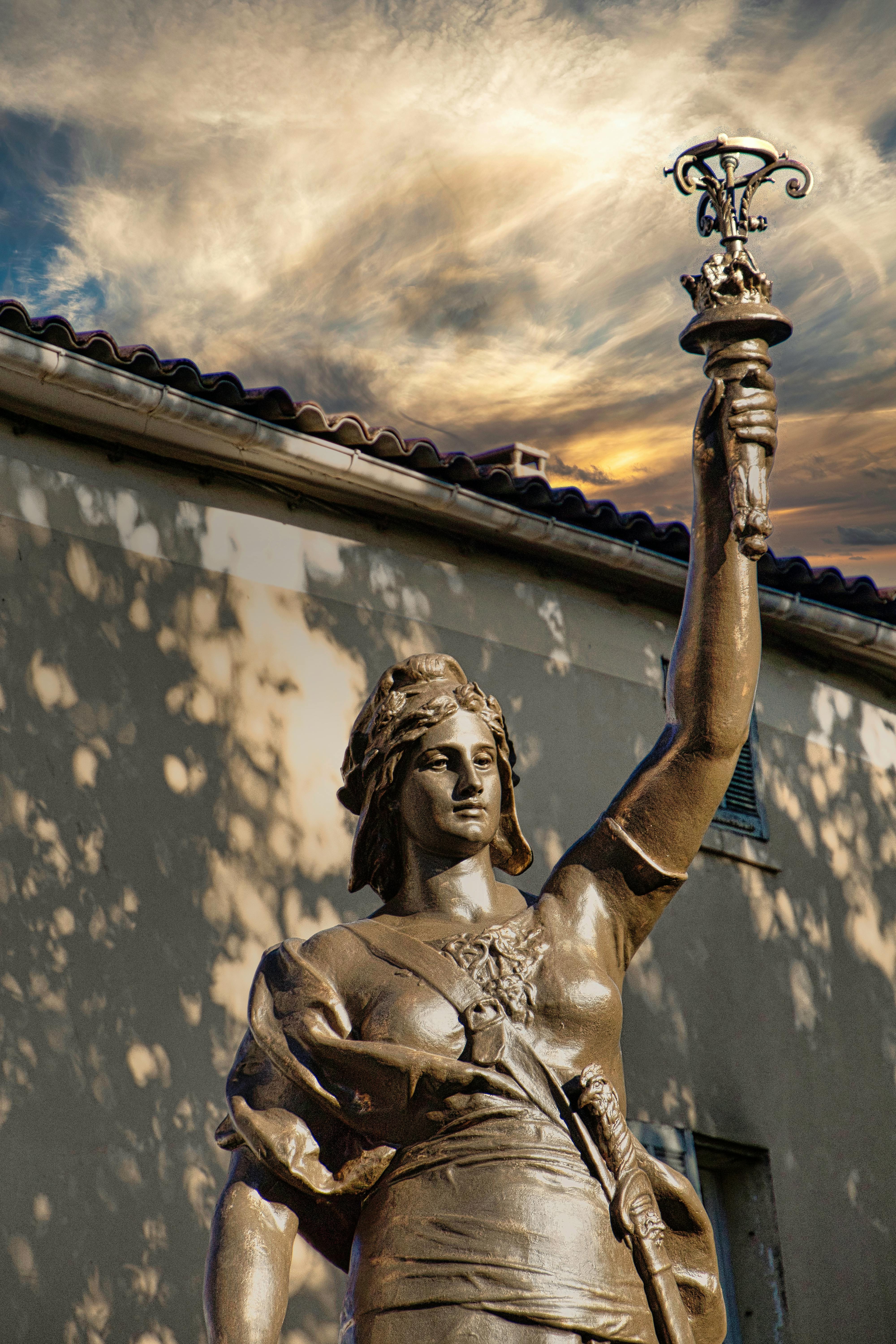 Bronze Statue of Person Holding Torch in Raised Arm · Free Stock Photo