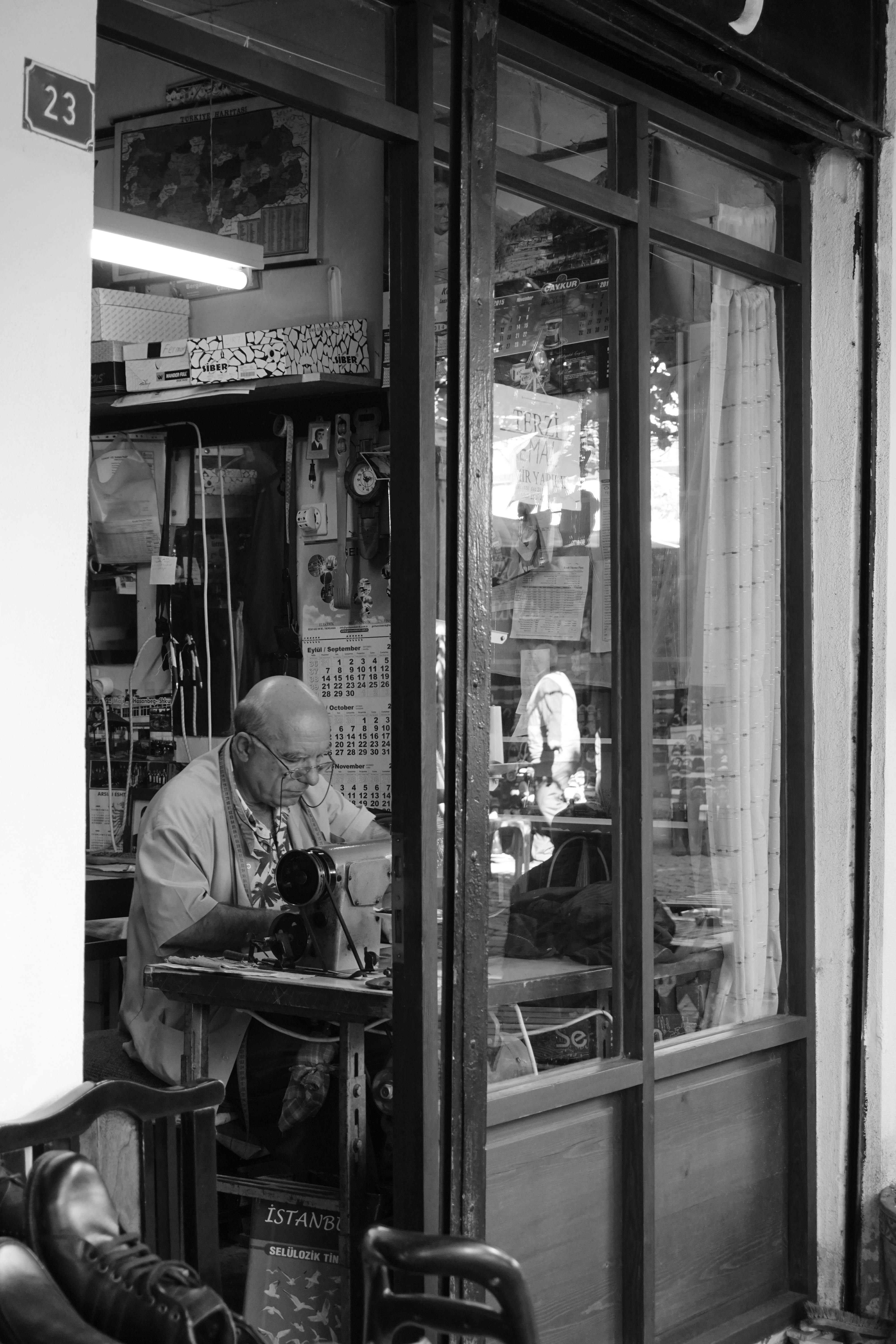 Elderly Tailor Sitting and Working behind Windows · Free Stock Photo