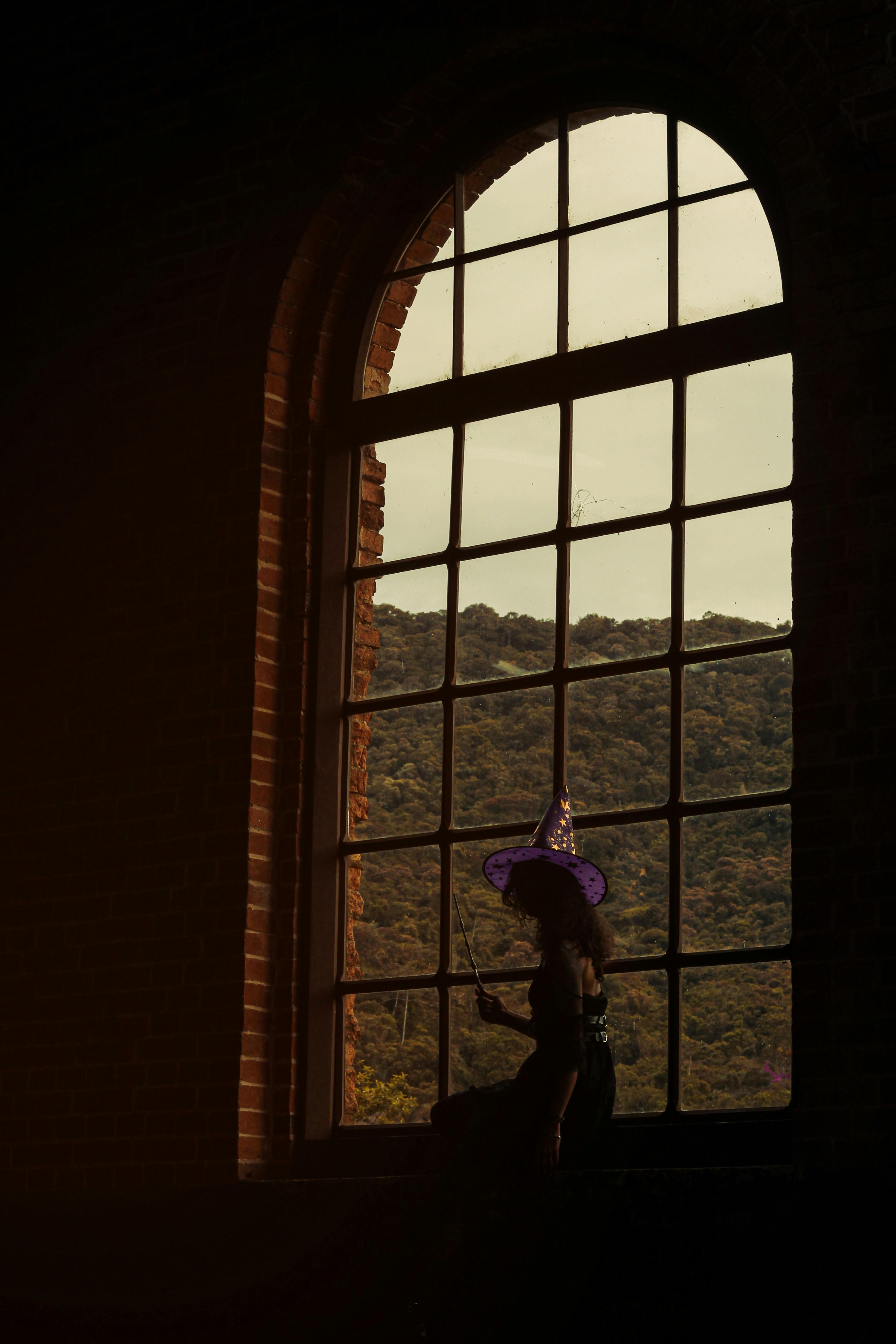 Witch with a Wand Sitting on a Large Arched Window · Free Stock Photo