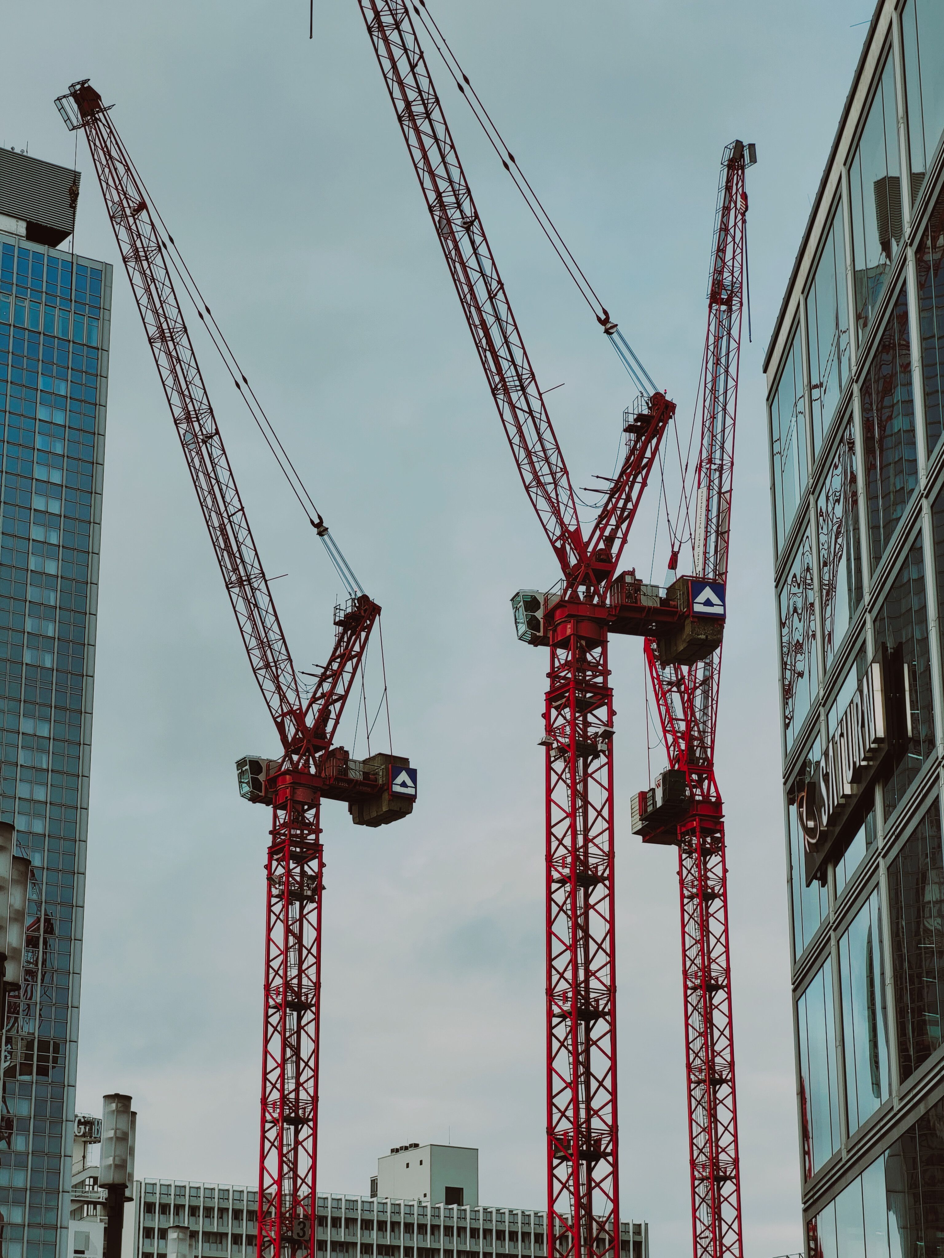 Three red cranes are standing in front of tall buildings · Free Stock Photo