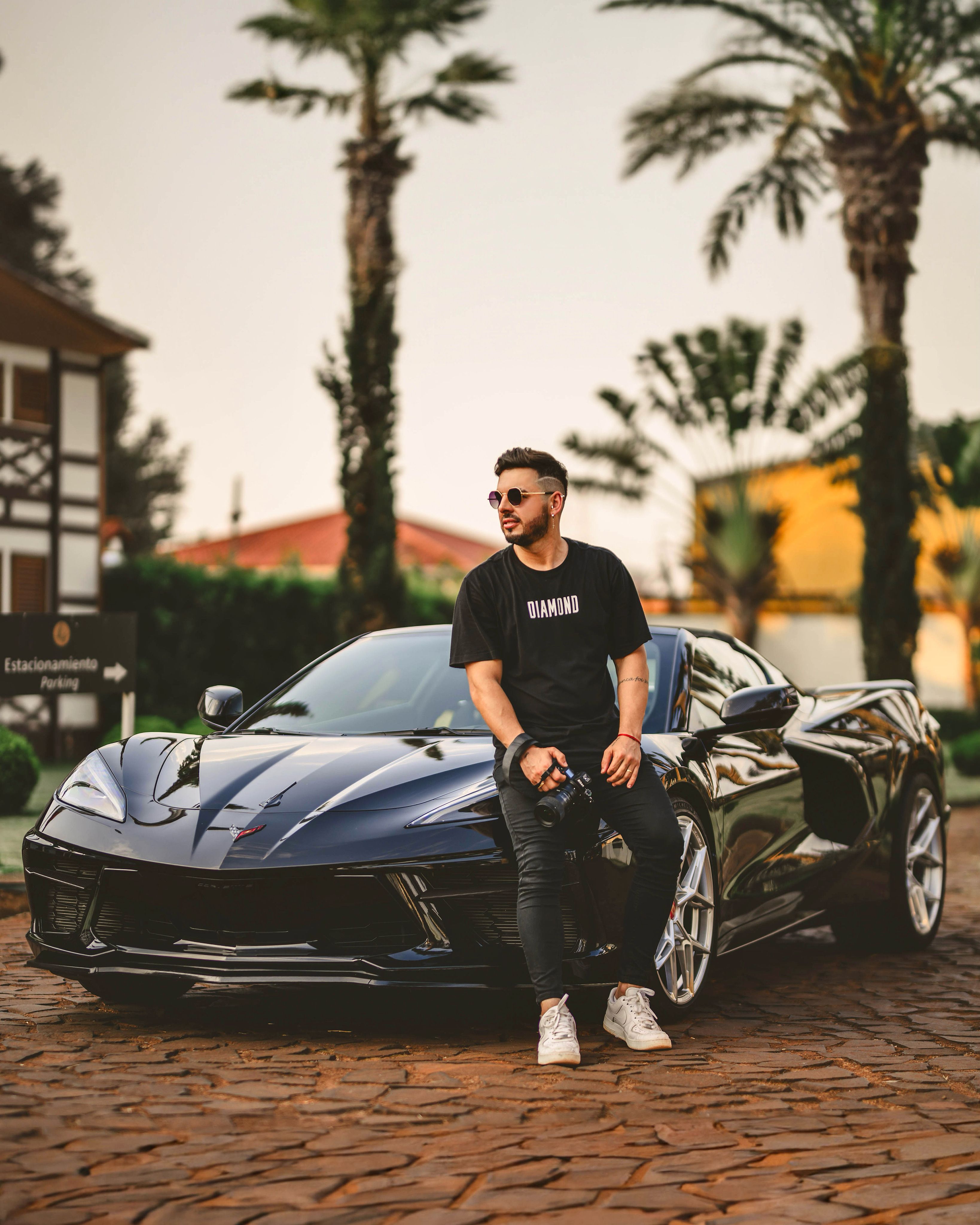 Man with a Camera Sitting on the Hood of a Black Chevrolet Corvette C8 ...