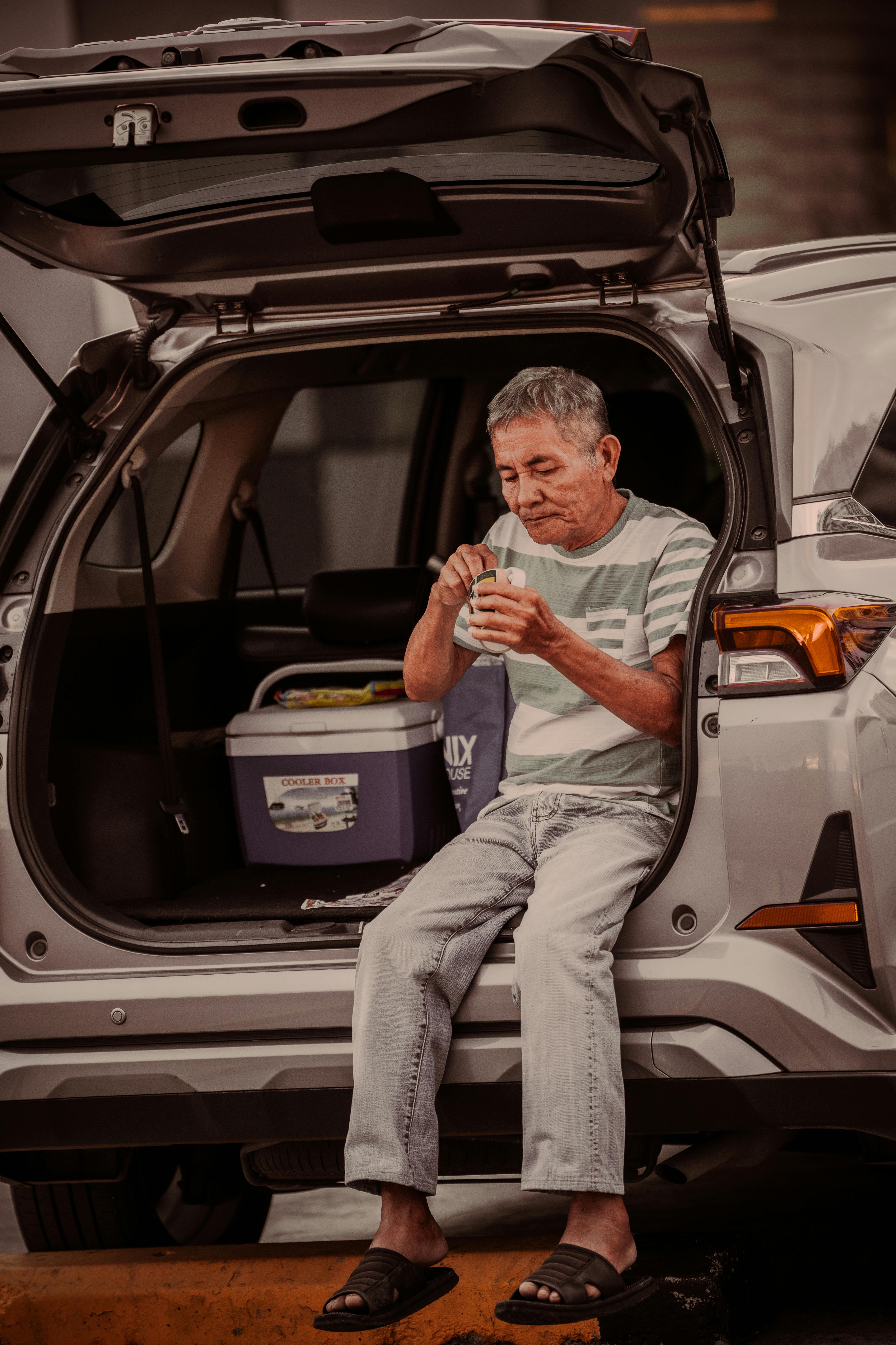 Elderly Man Sitting in Car Trunk and Eating Food · Free Stock Photo
