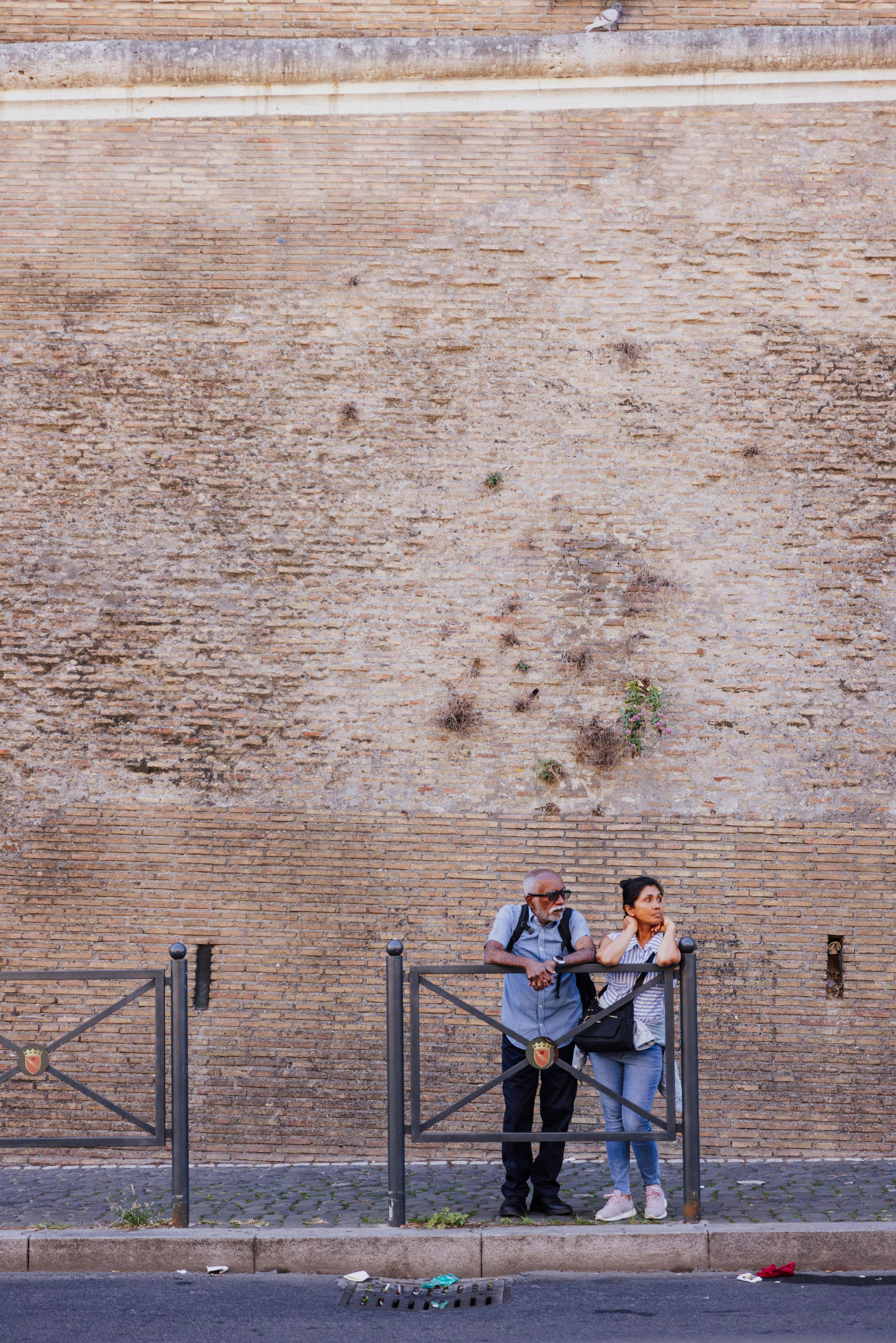 Woman and Man Standing on Railing with Stone Wall behind · Free Stock Photo