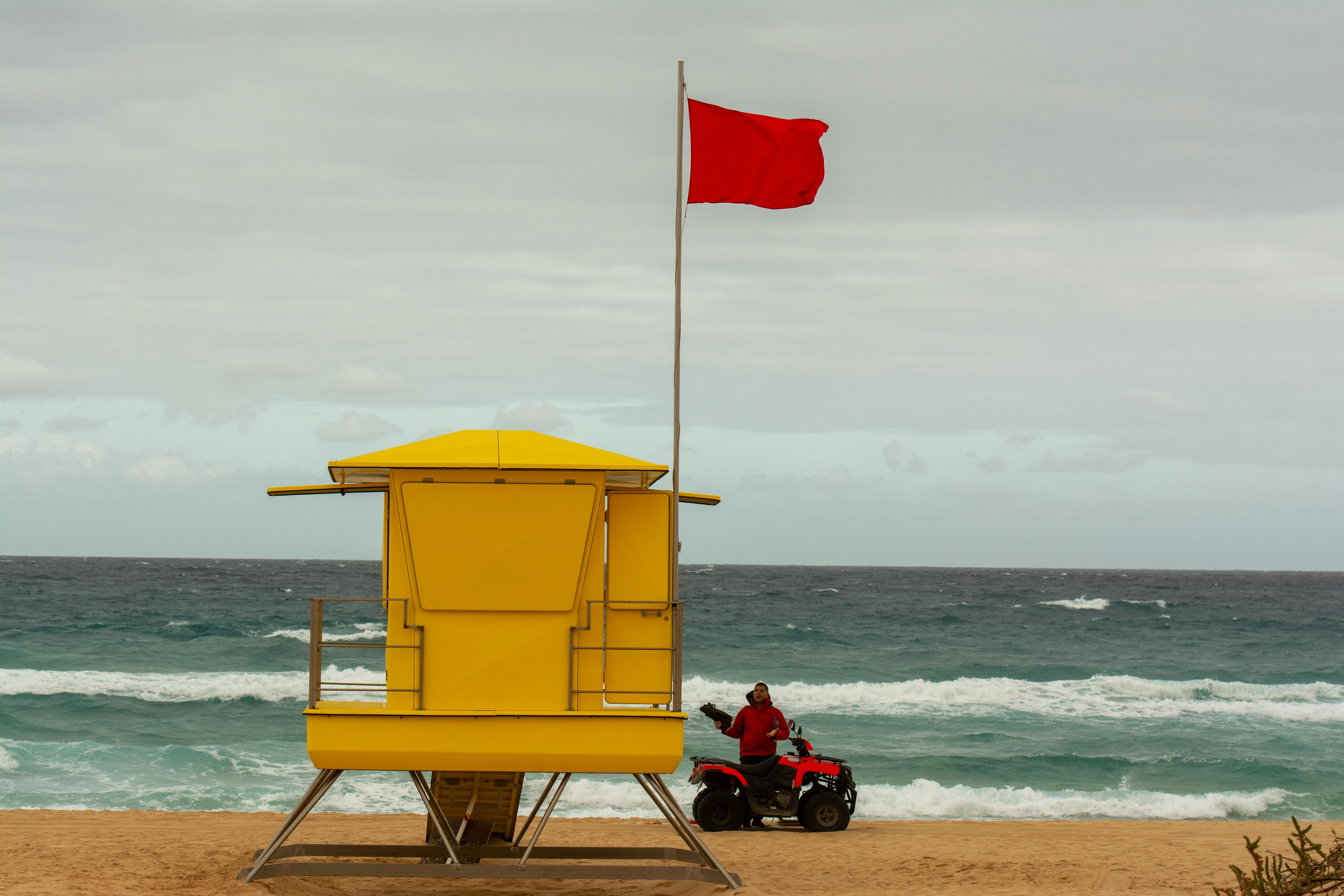 Man by a Quad Bike Talking to a Lifeguard in Yellow Booth with Red Flag ...