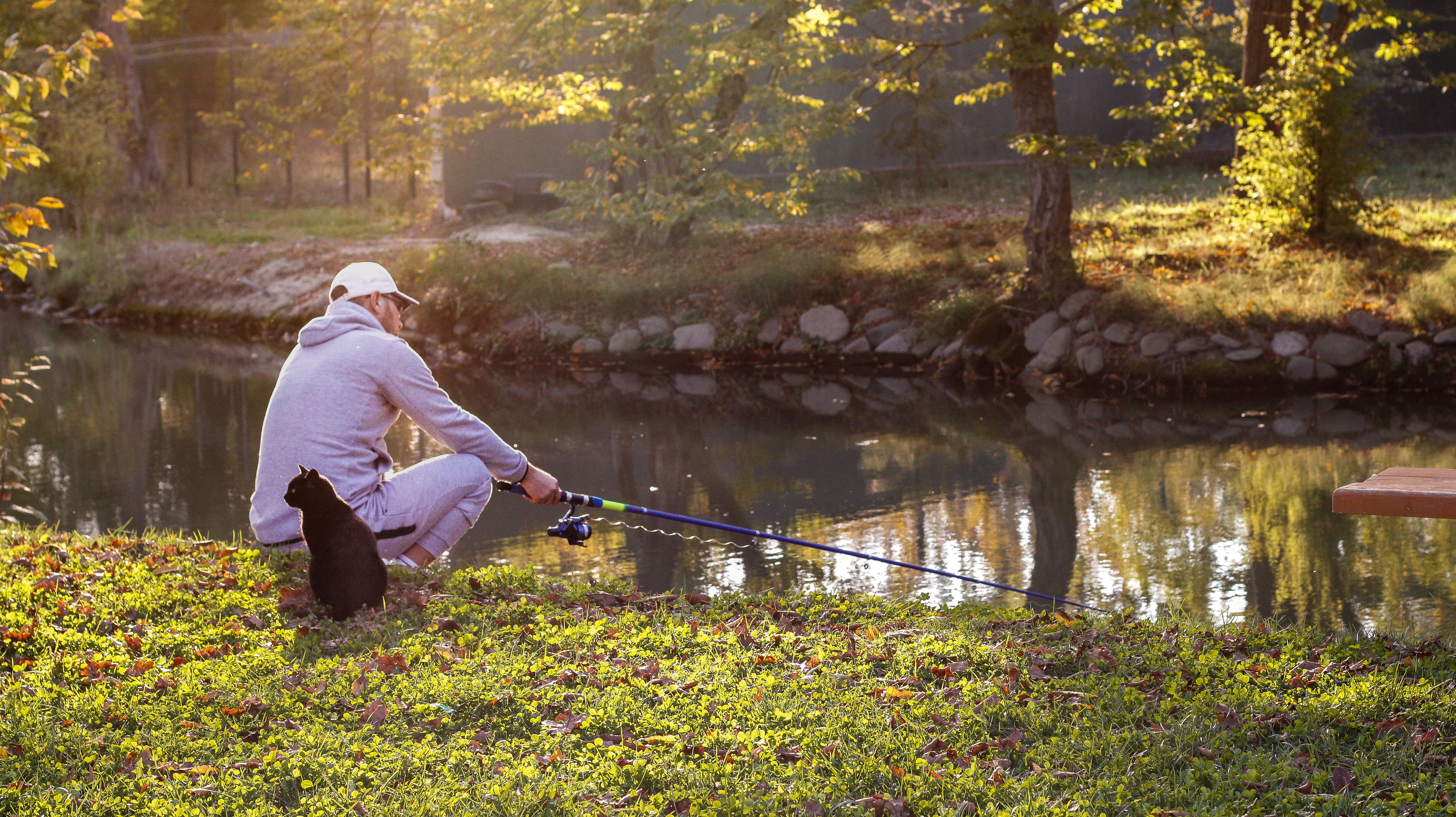 Angler with a Black Cat Fishing in the River · Free Stock Photo