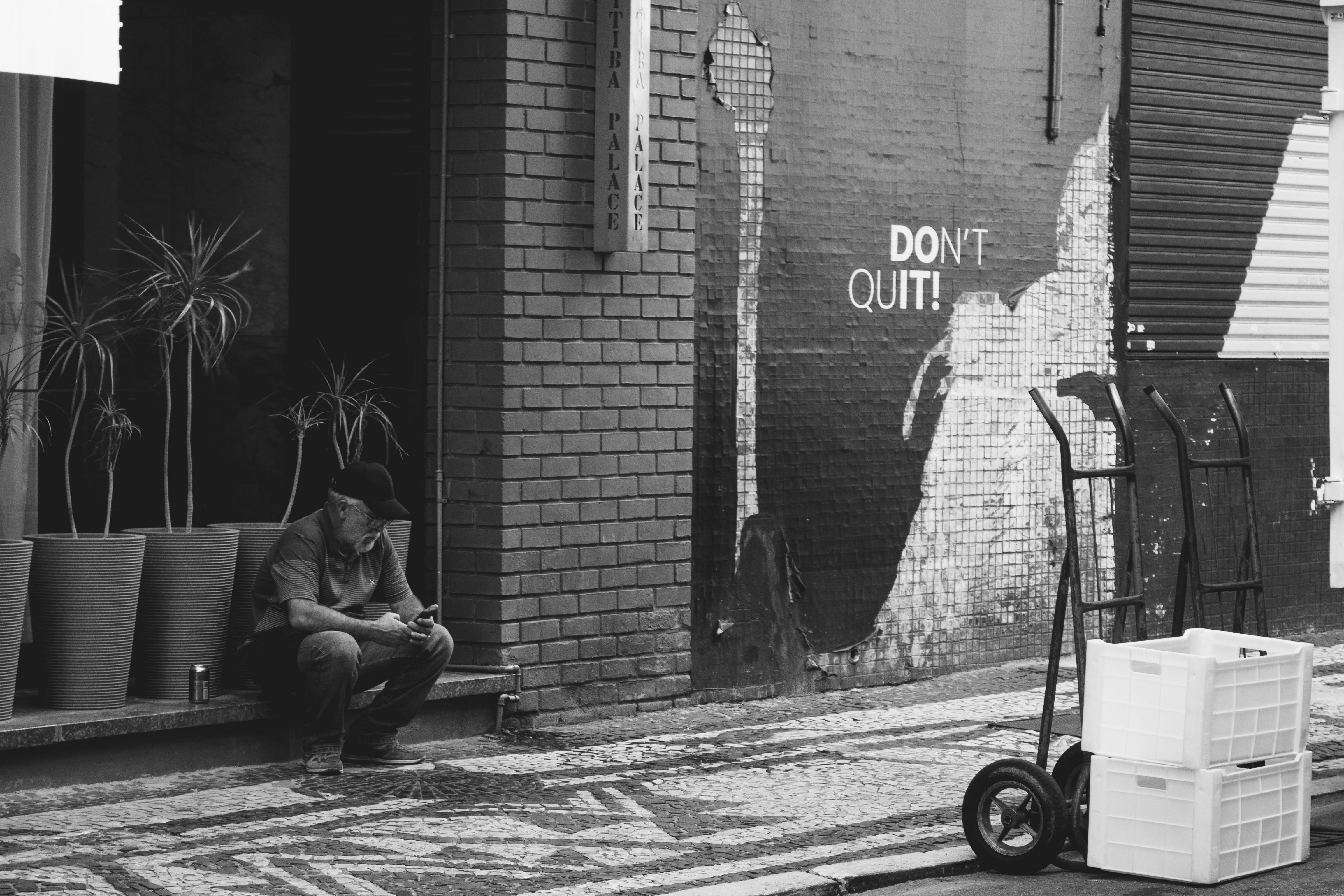 Man Sitting with a Smartphone Near Transport Trolleys · Free Stock Photo