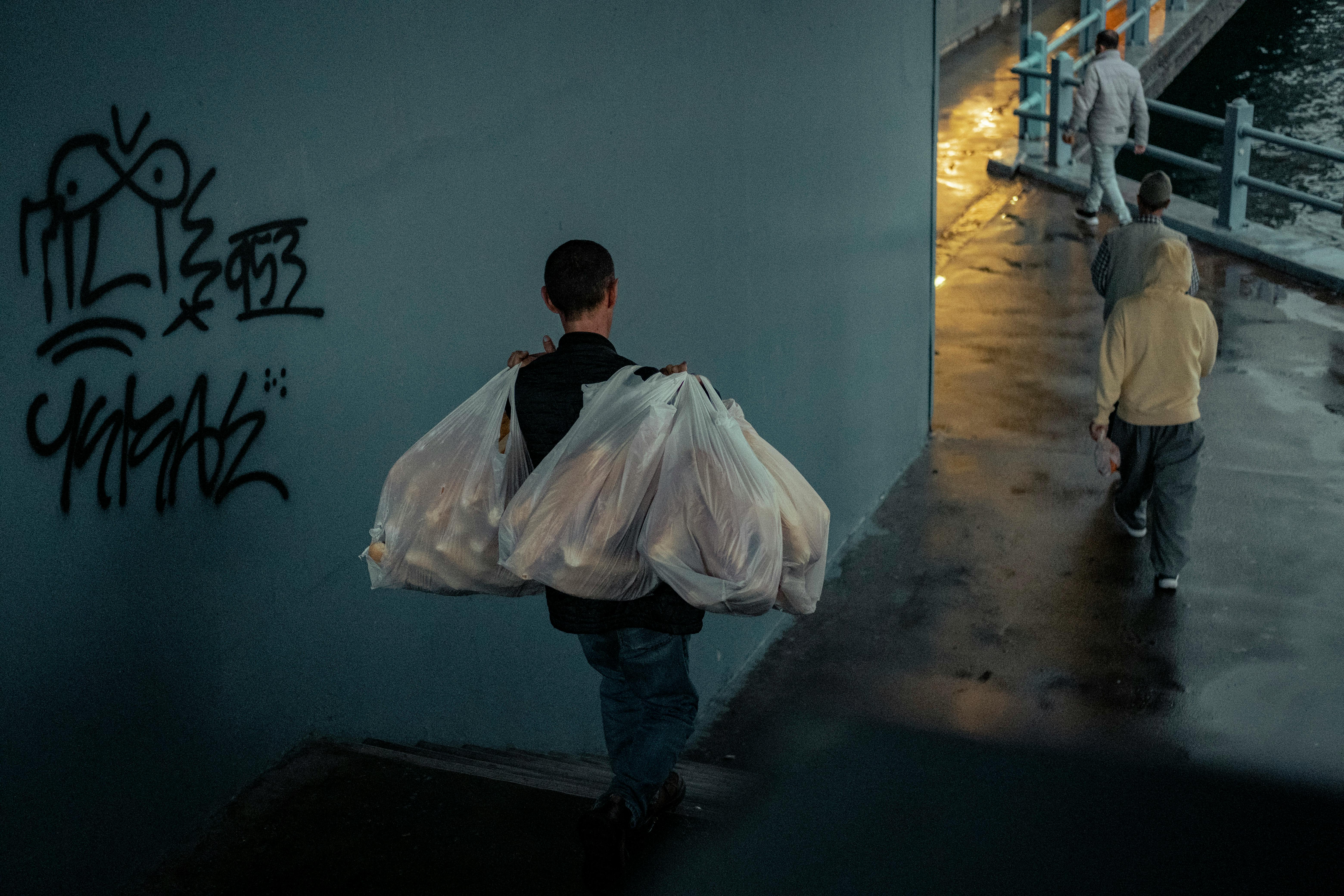Back View of a Man Walking with Full Plastic Bags · Free Stock Photo