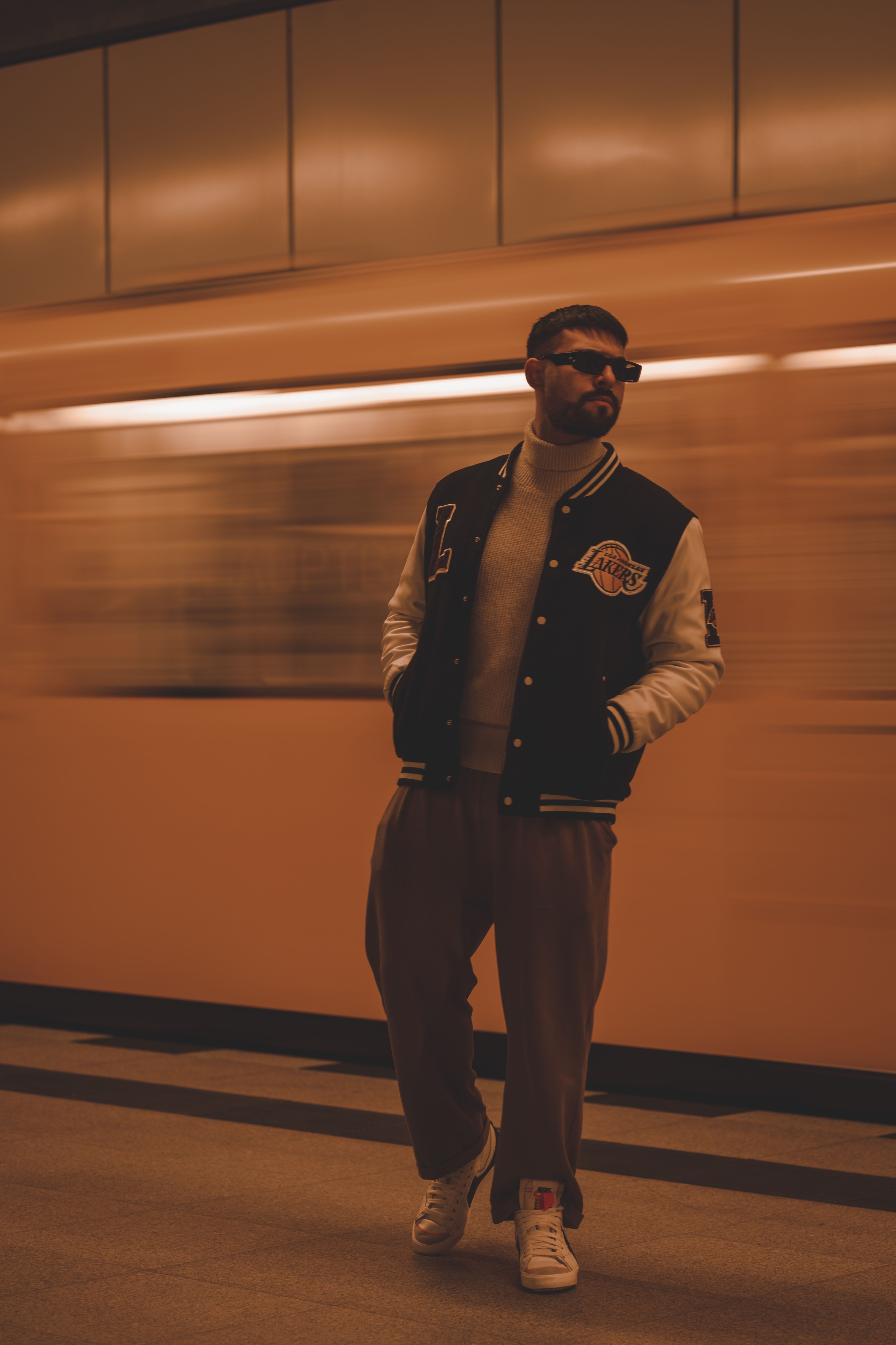 Model in Varsity Jacket over a Turtleneck and Loose Pants on a Subway ...