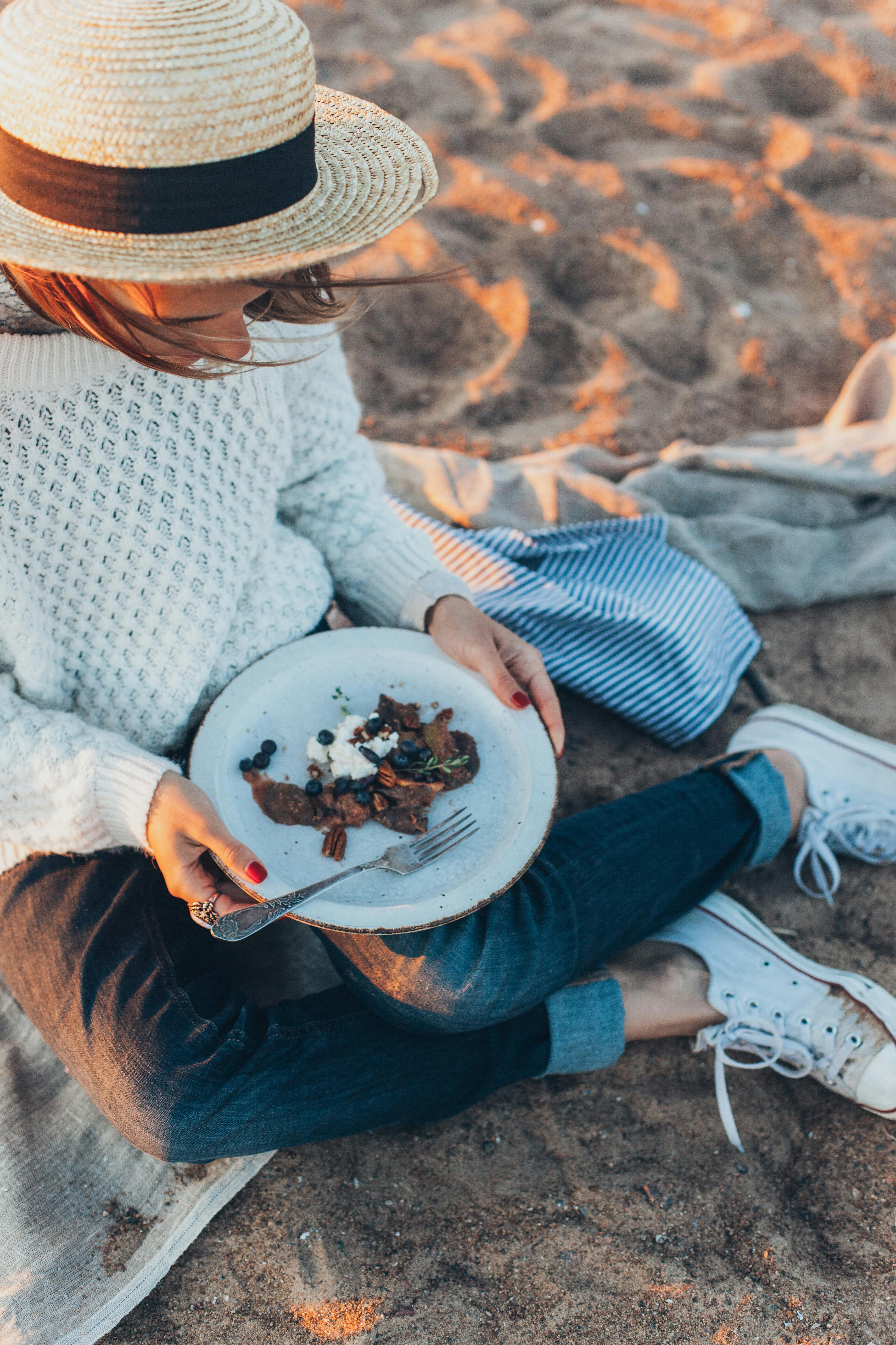 Woman Holding Plate While Sitting on Sand · Free Stock Photo
