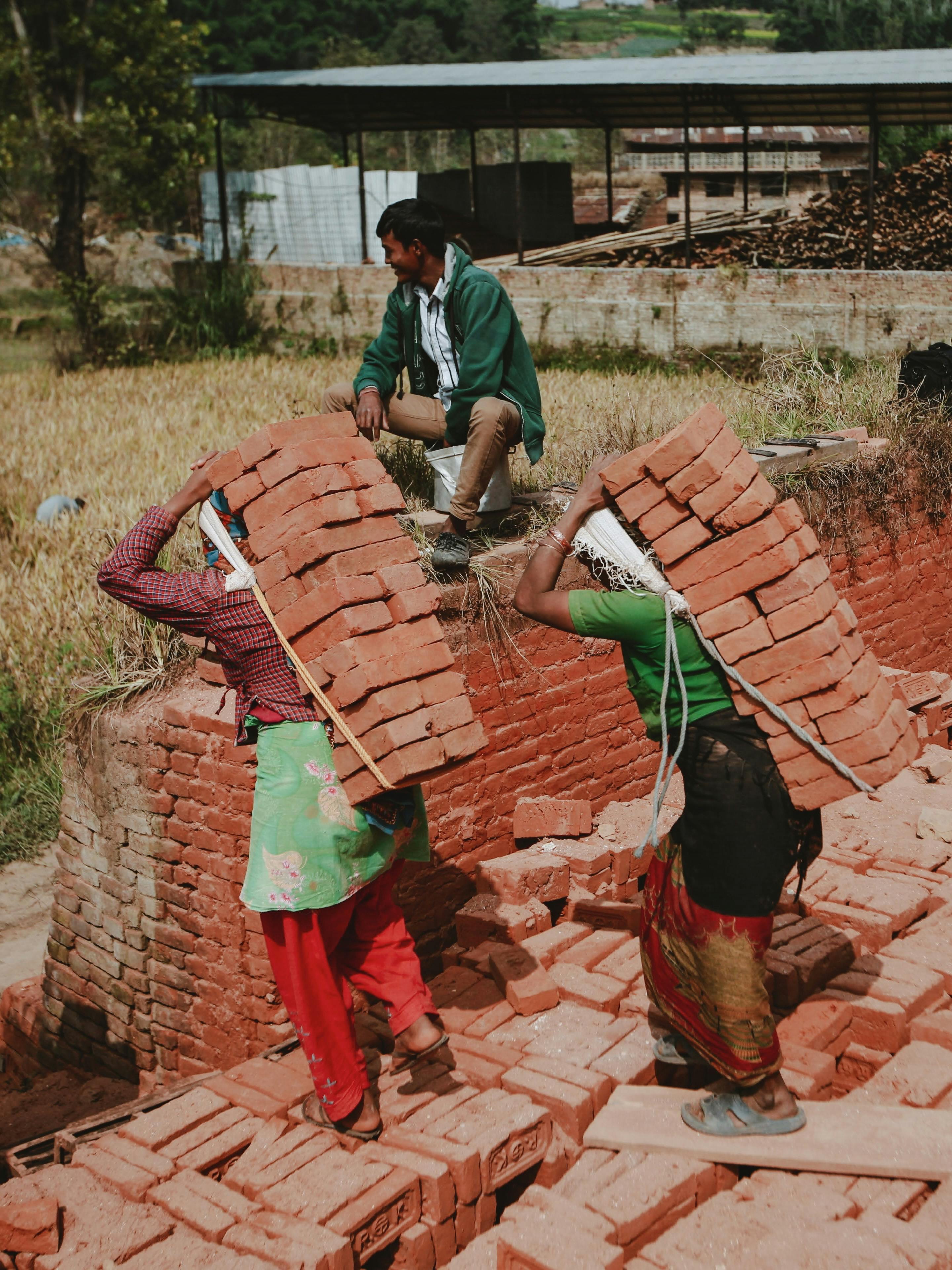 Men Working at a Construction Site Carrying Bricks on Their Backs ...