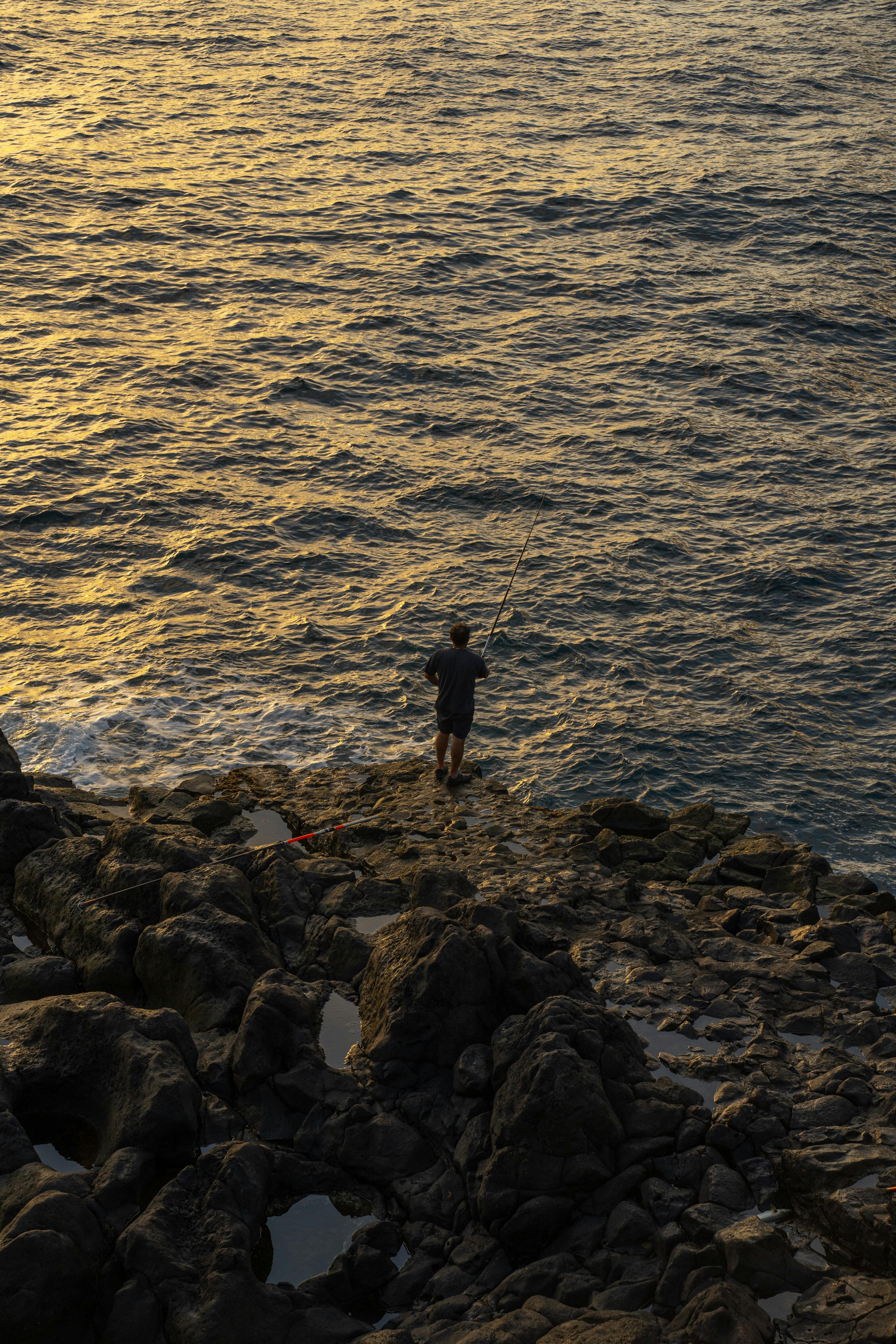 Aerial View of a Man Fishing in the Sea at Sunset · Free Stock Photo