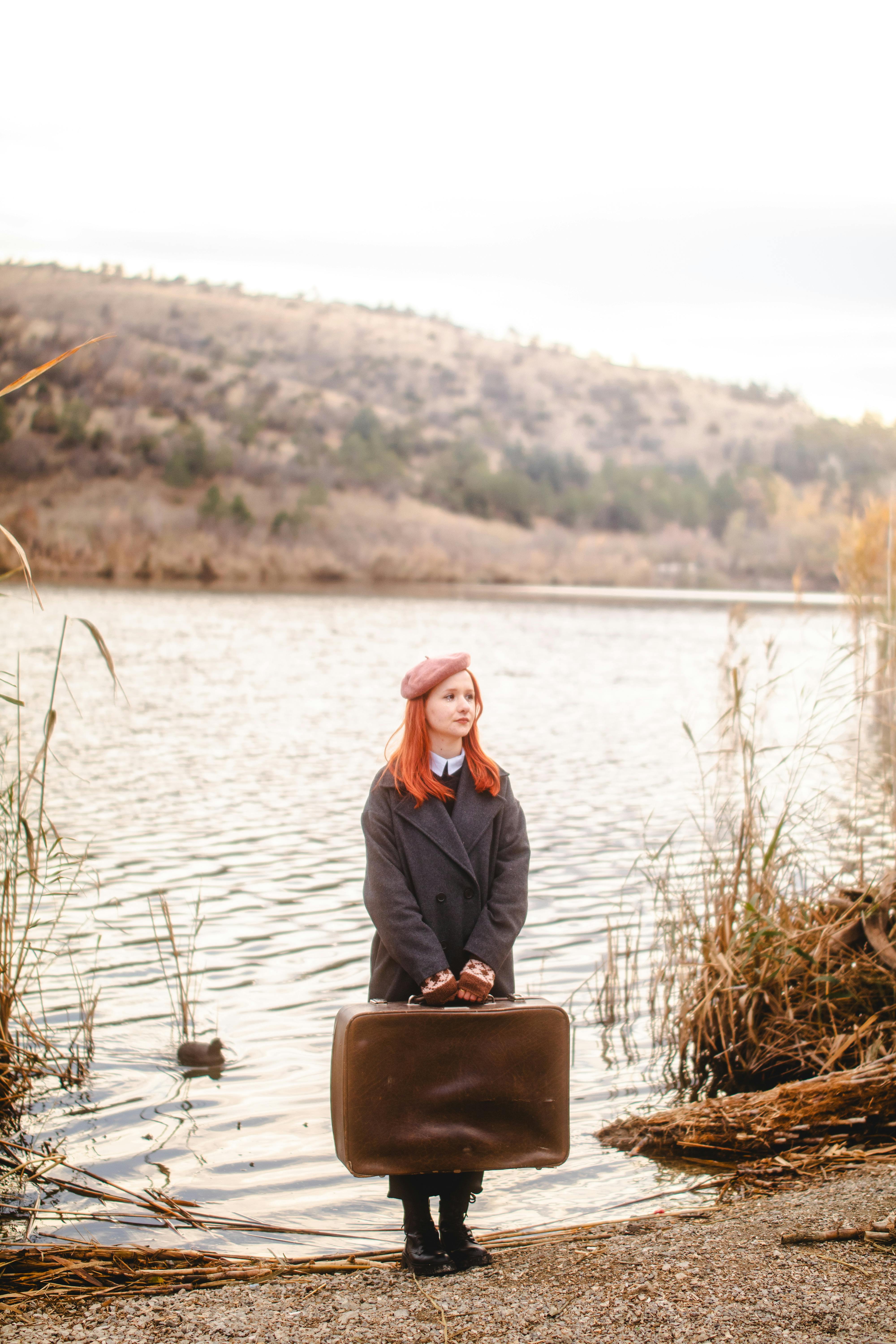 Young Woman Standing by a Body of Water with an Old Suitcase · Free ...