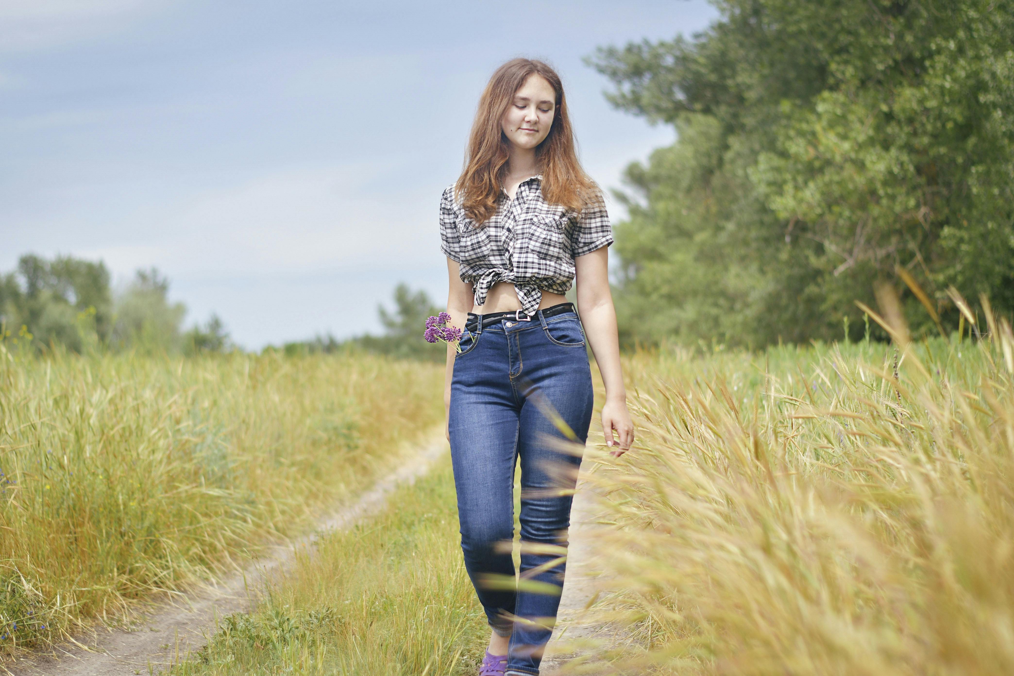 Photo of a Girl Wearing Jeans Walking in a Field · Free Stock Photo