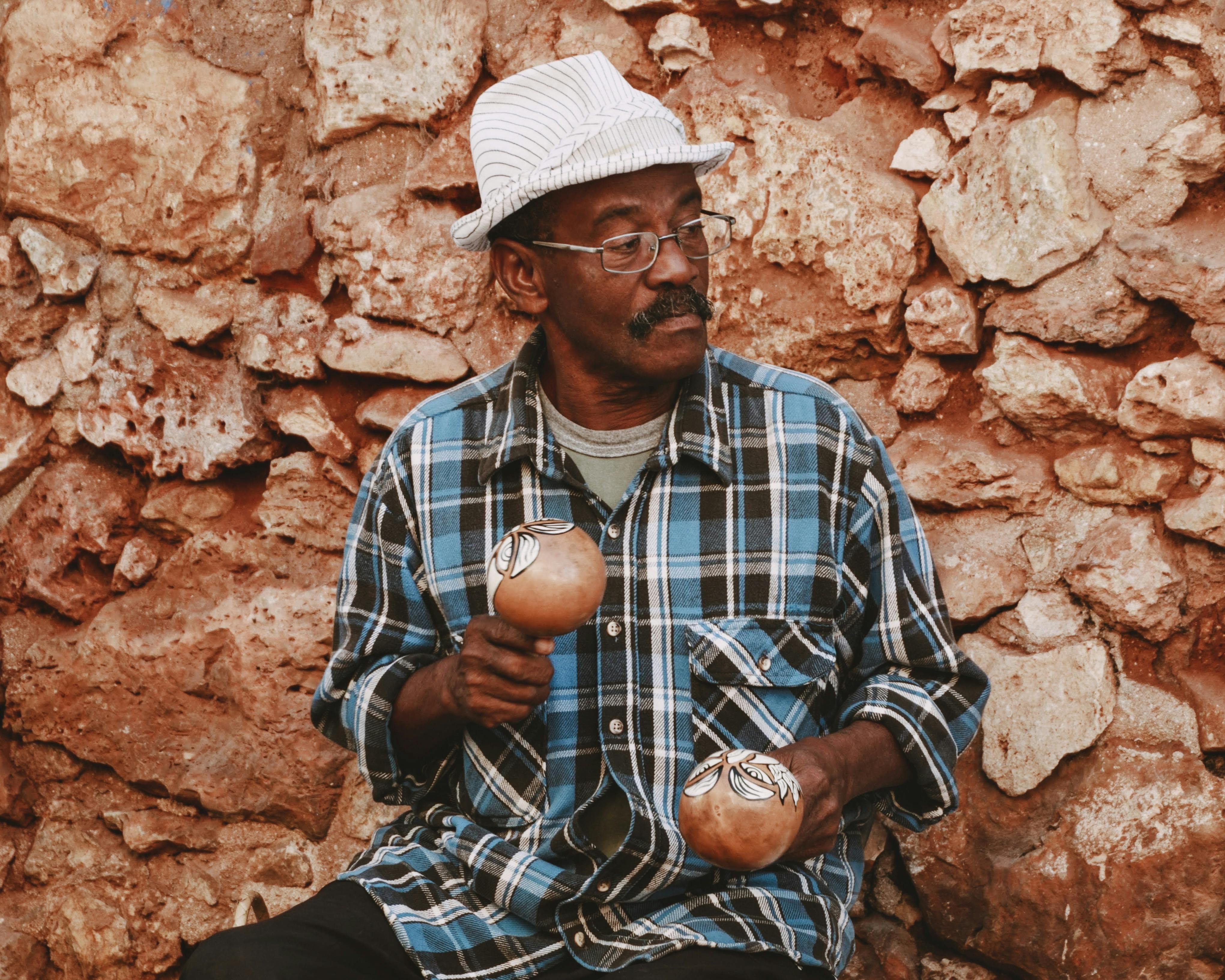 Man Playing Maracas Sitting by a Stone Wall · Free Stock Photo