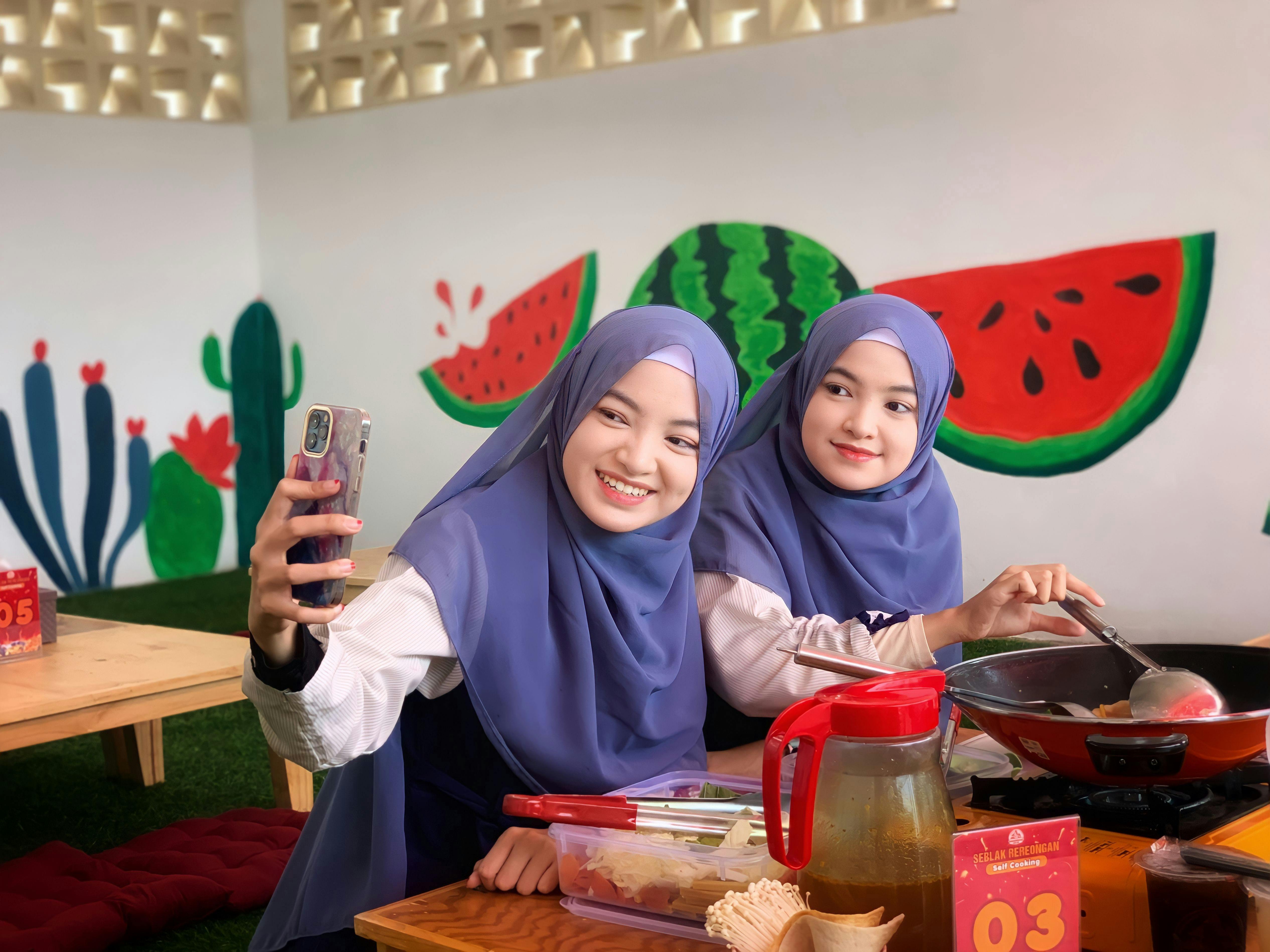 Two women in hijabs sitting at a table with food · Free Stock Photo
