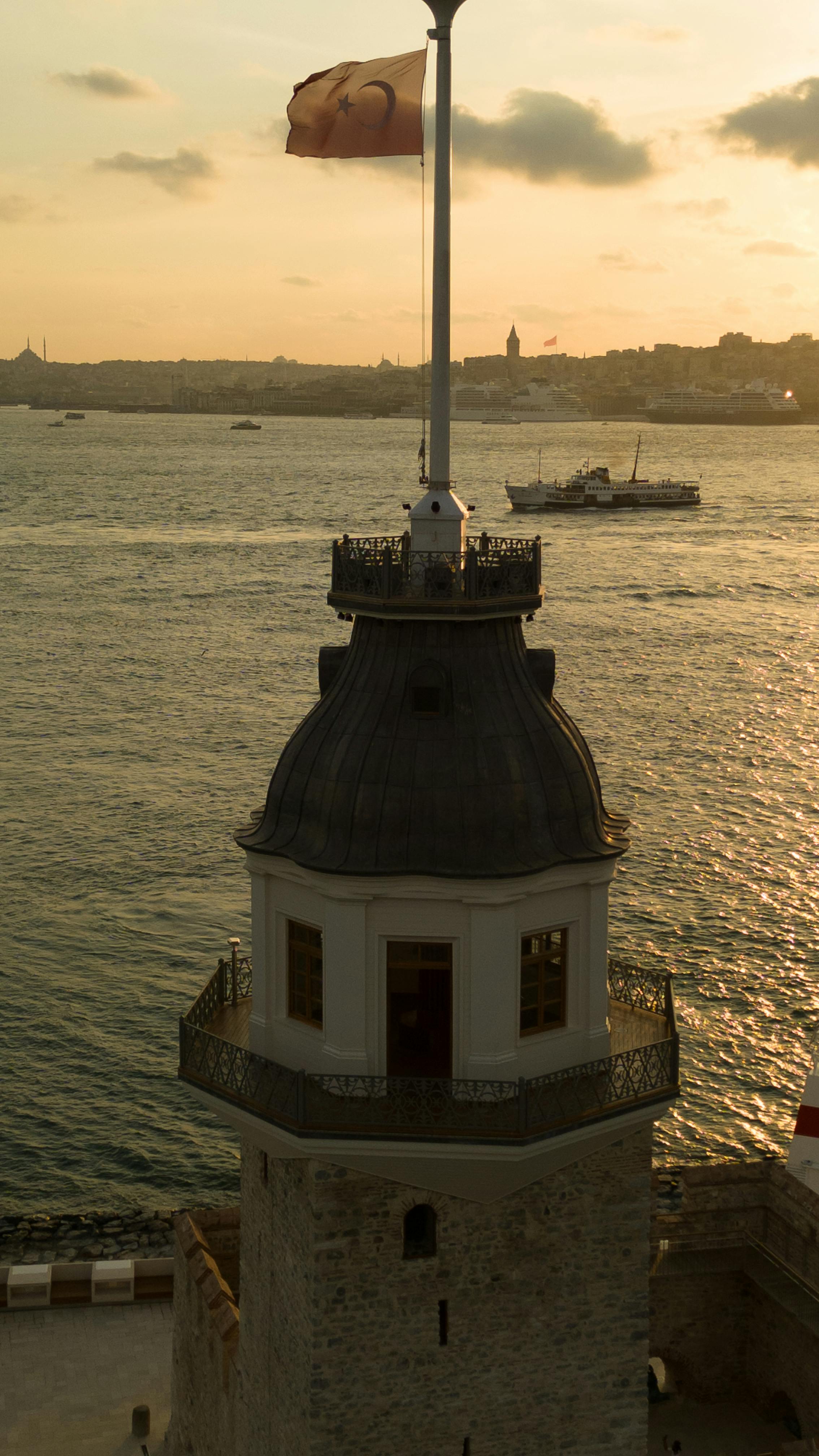A flag flying over a lighthouse at sunset · Free Stock Photo