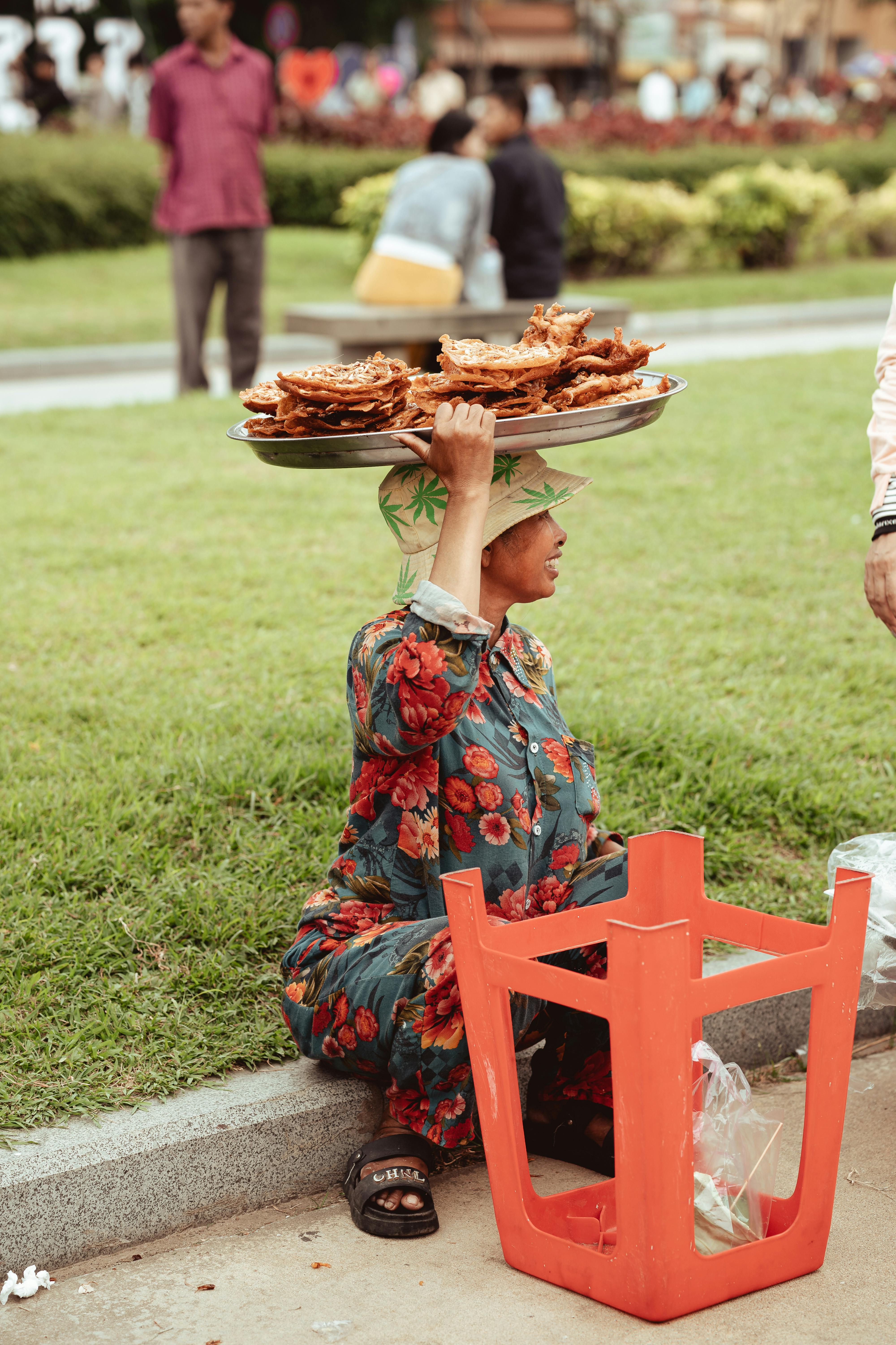 Street Food Vendor Sitting and Holding Tray on Head · Free Stock Photo