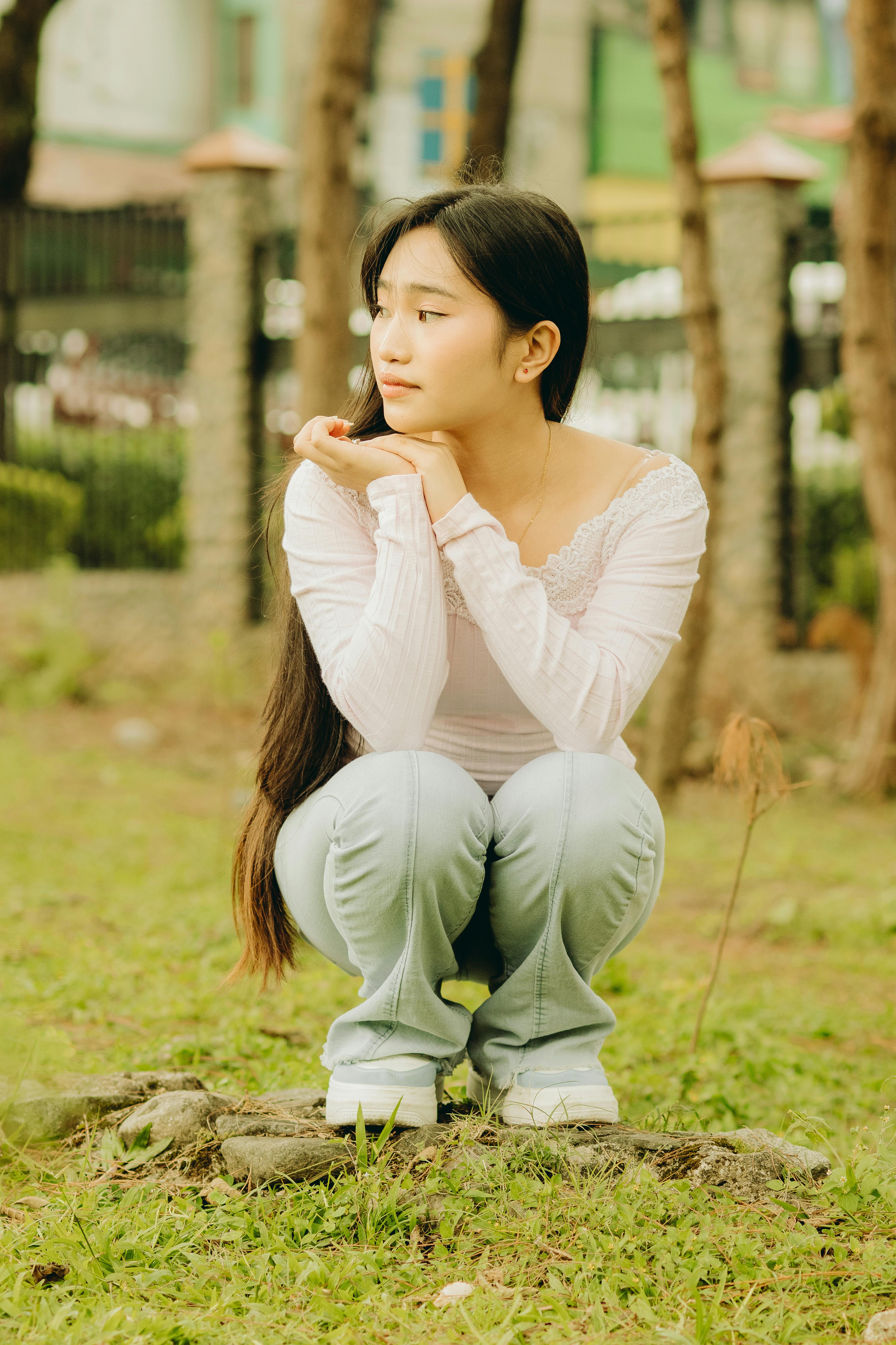 A young woman crouching down in the grass · Free Stock Photo