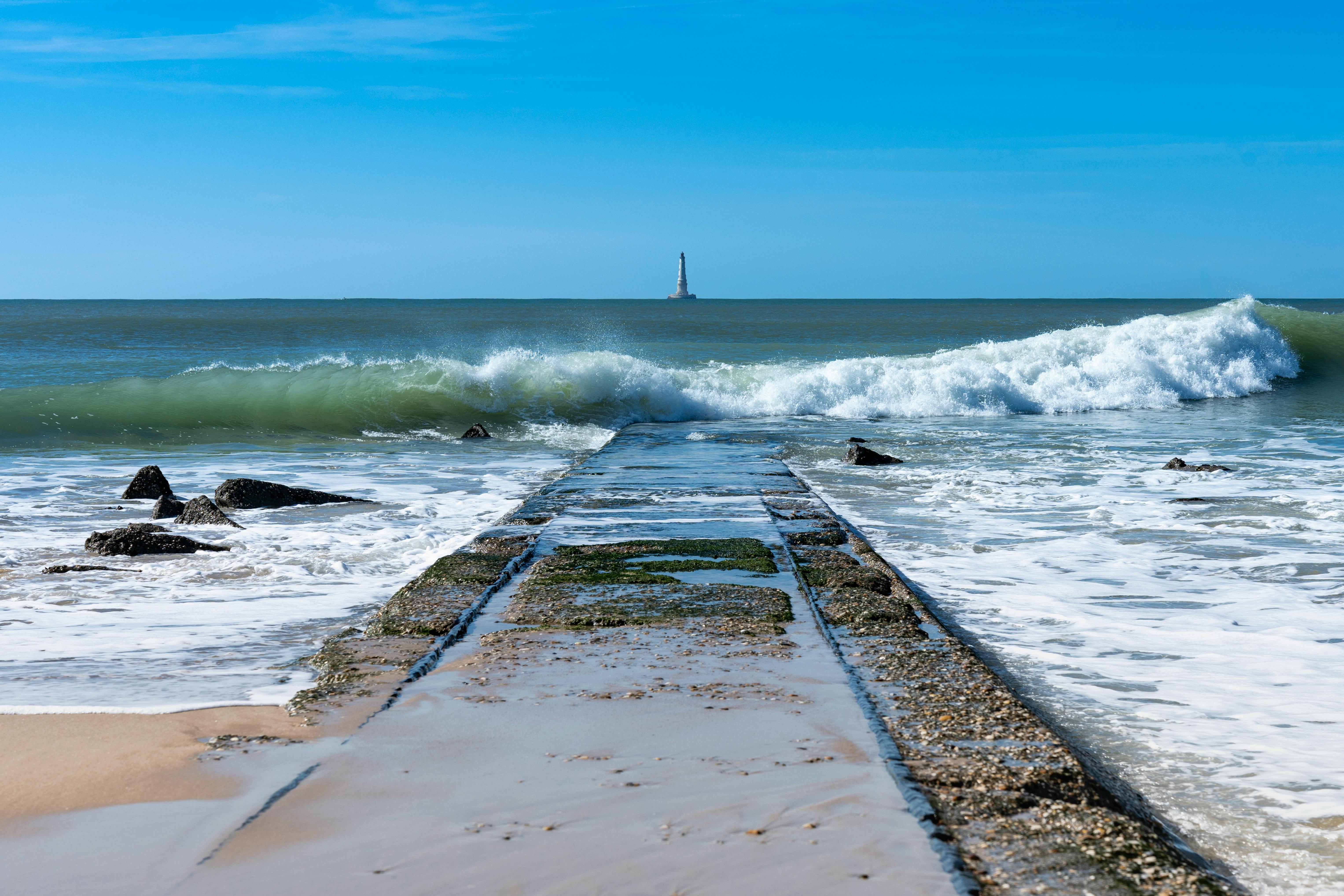 View of a Wave Washing up the Shore and a Lighthouse in Distance · Free ...