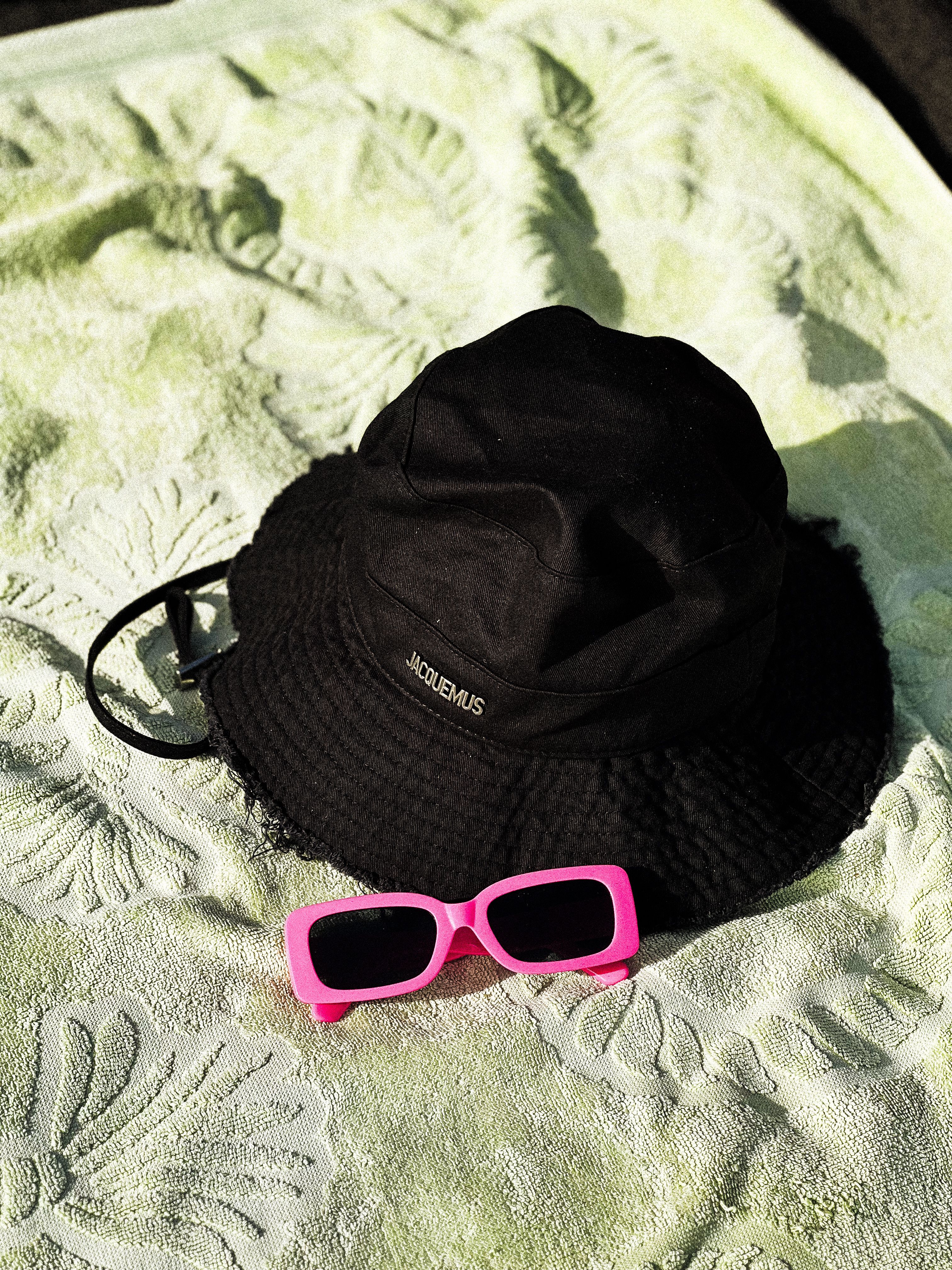 Black Bucket Hat and Pink Sunglasses Set on Beach Towel · Free Stock Photo