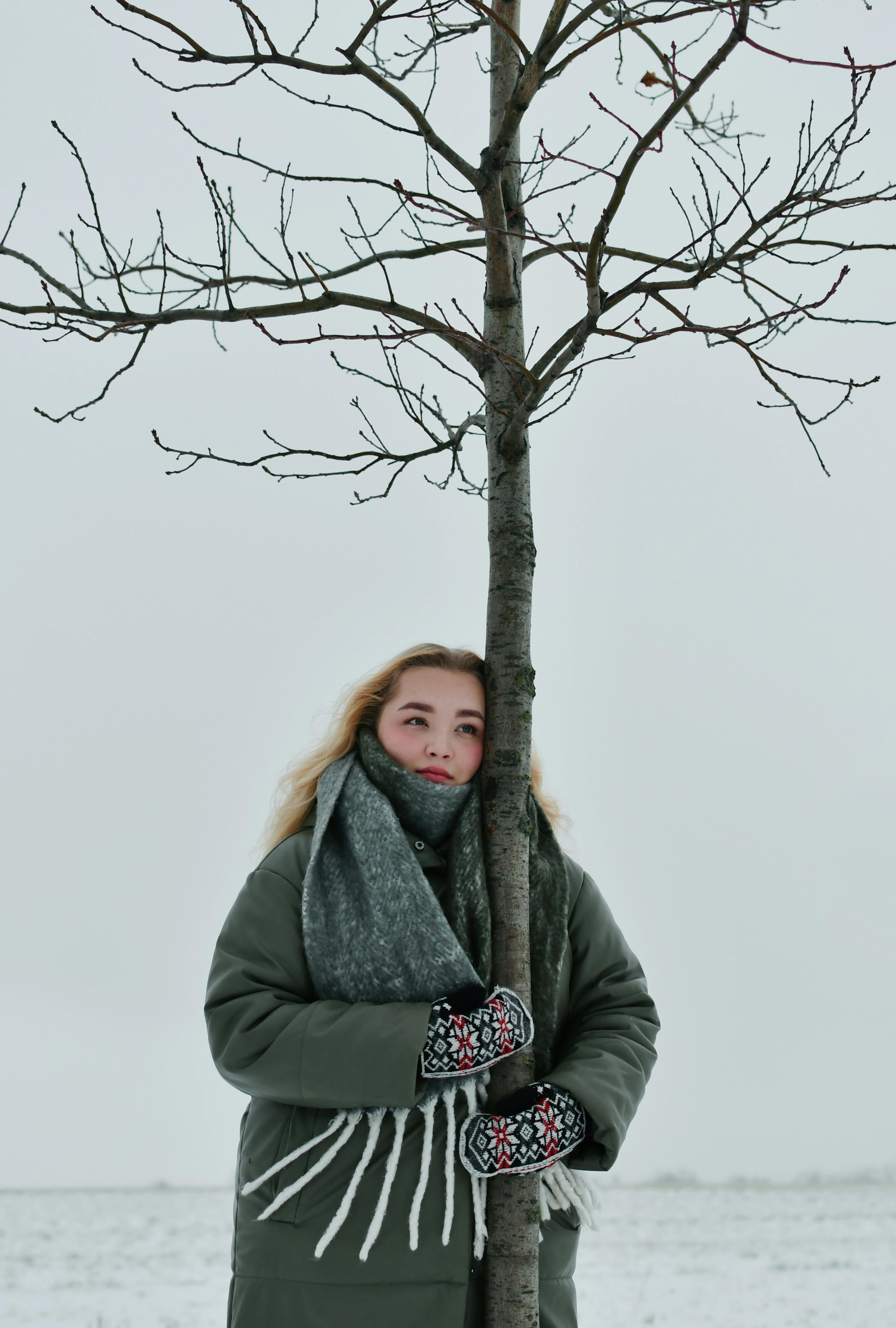 Blonde Woman in Jacket Holding Tree · Free Stock Photo