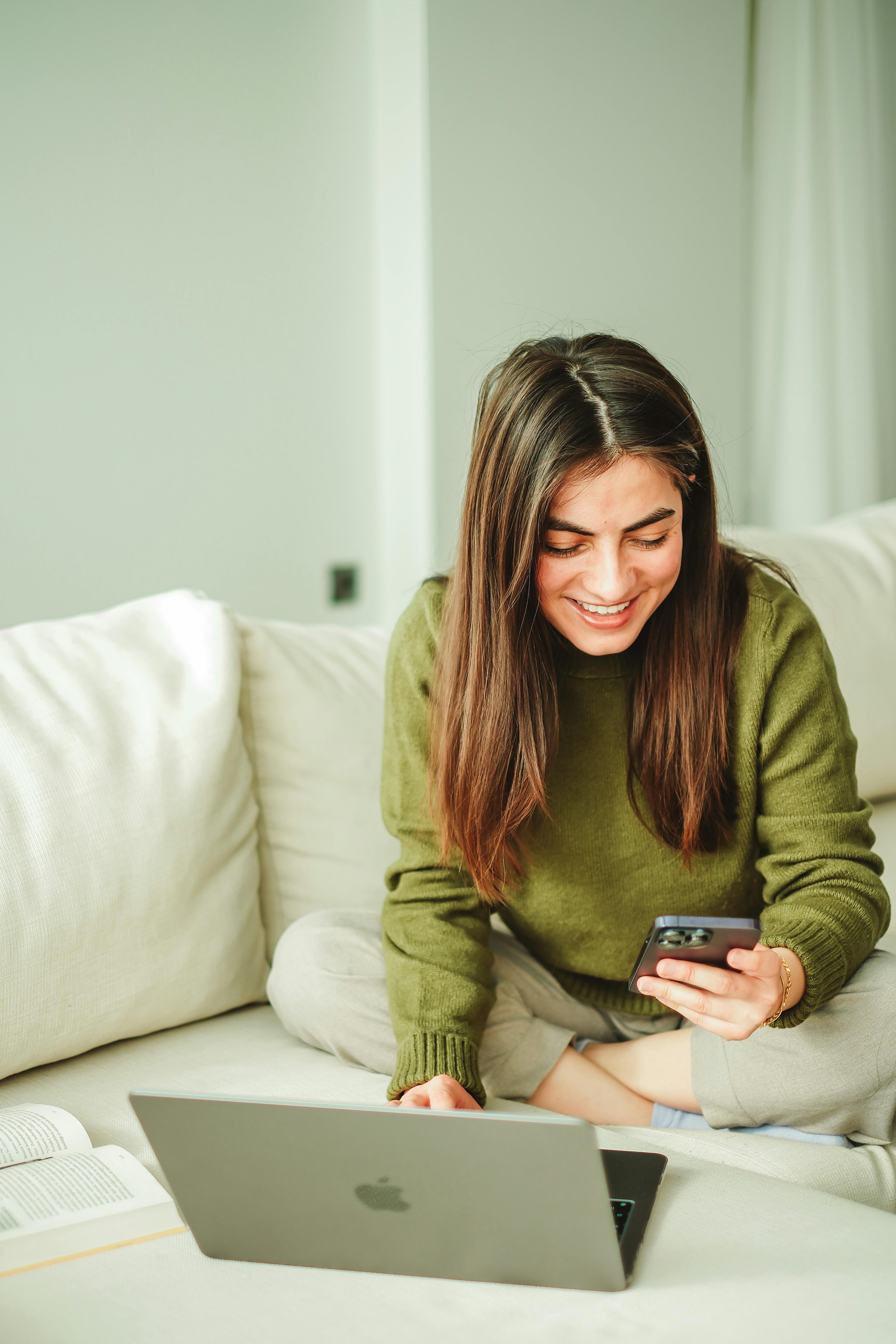 Young Woman Using a Laptop and Smartphone Sitting on Sofa · Free Stock ...
