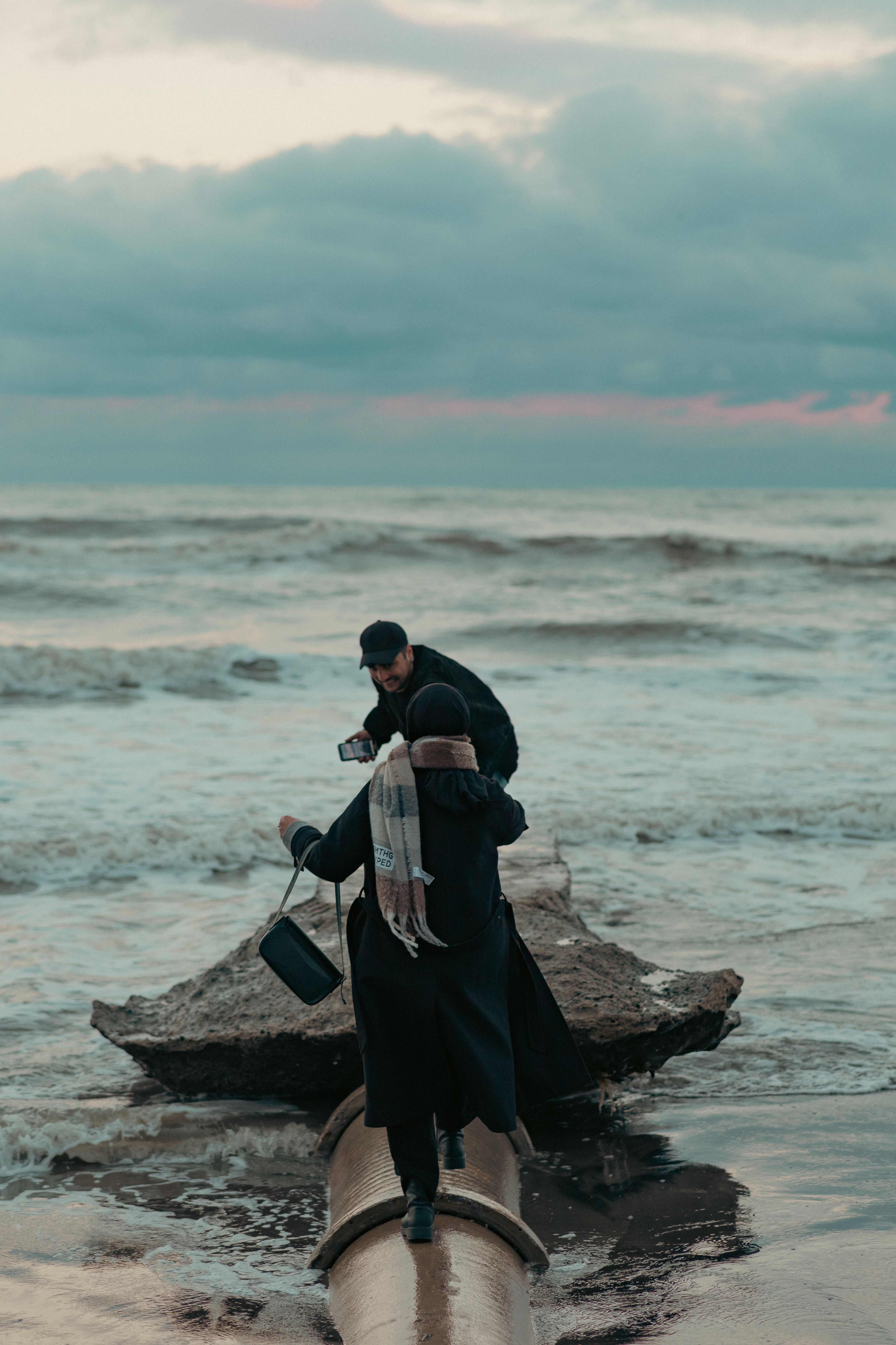 Man and Woman Walking on a Pipe and Rock on the Shore · Free Stock Photo