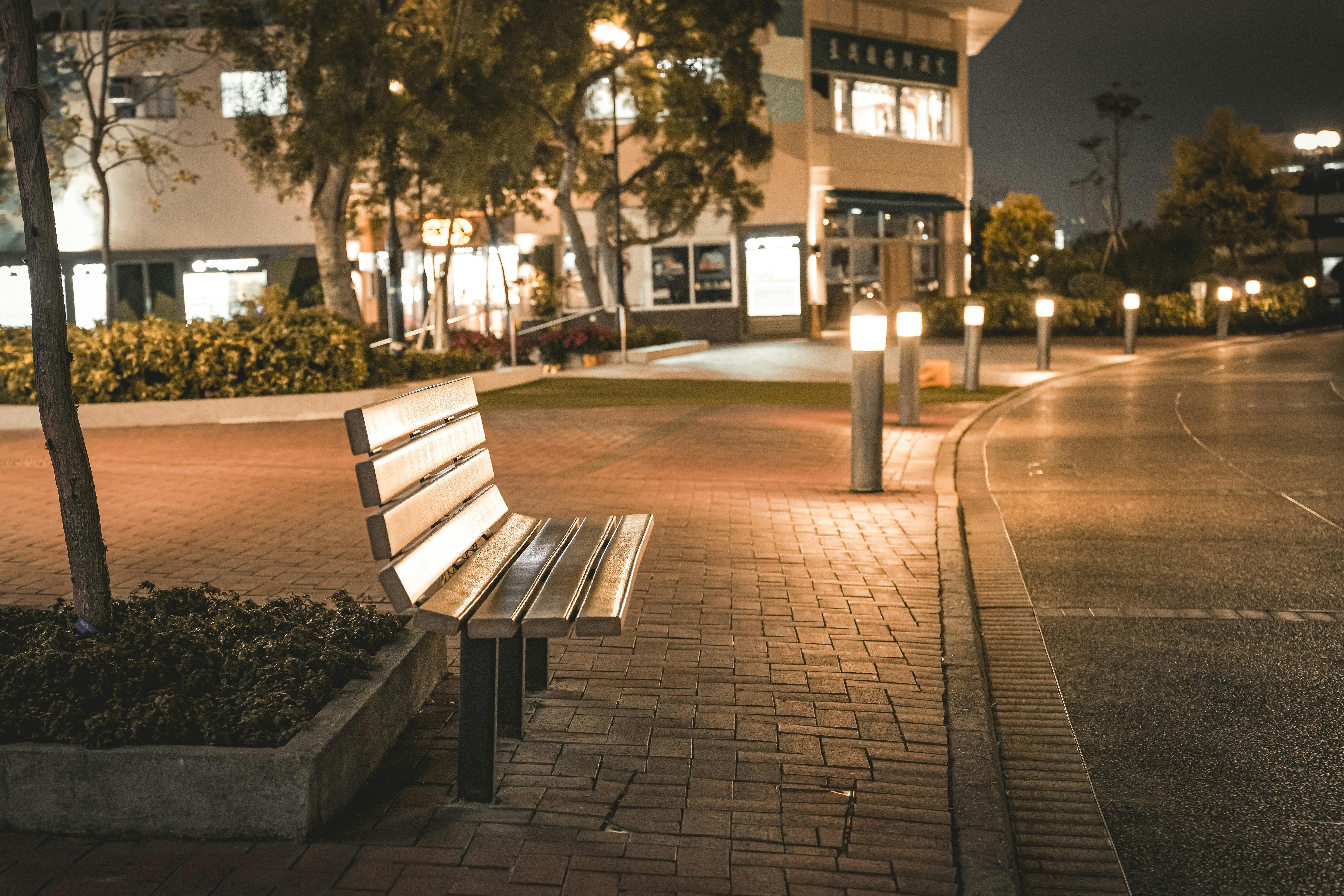 An Empty Bench and Illuminated Bollards on the Sidewalk in City in the Evening · Free Stock Photo