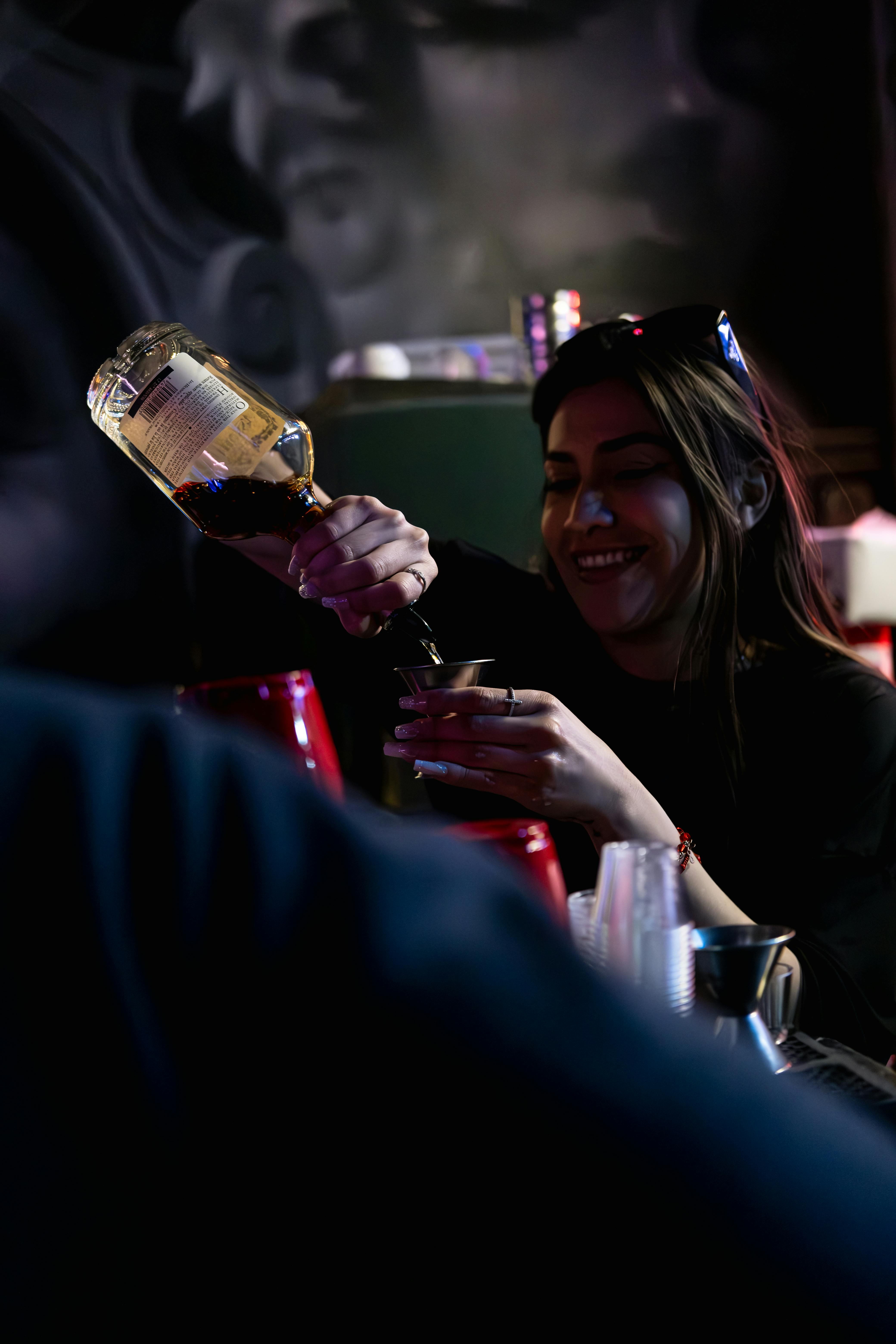 Smiling Woman Pouring Alcohol at Night · Free Stock Photo