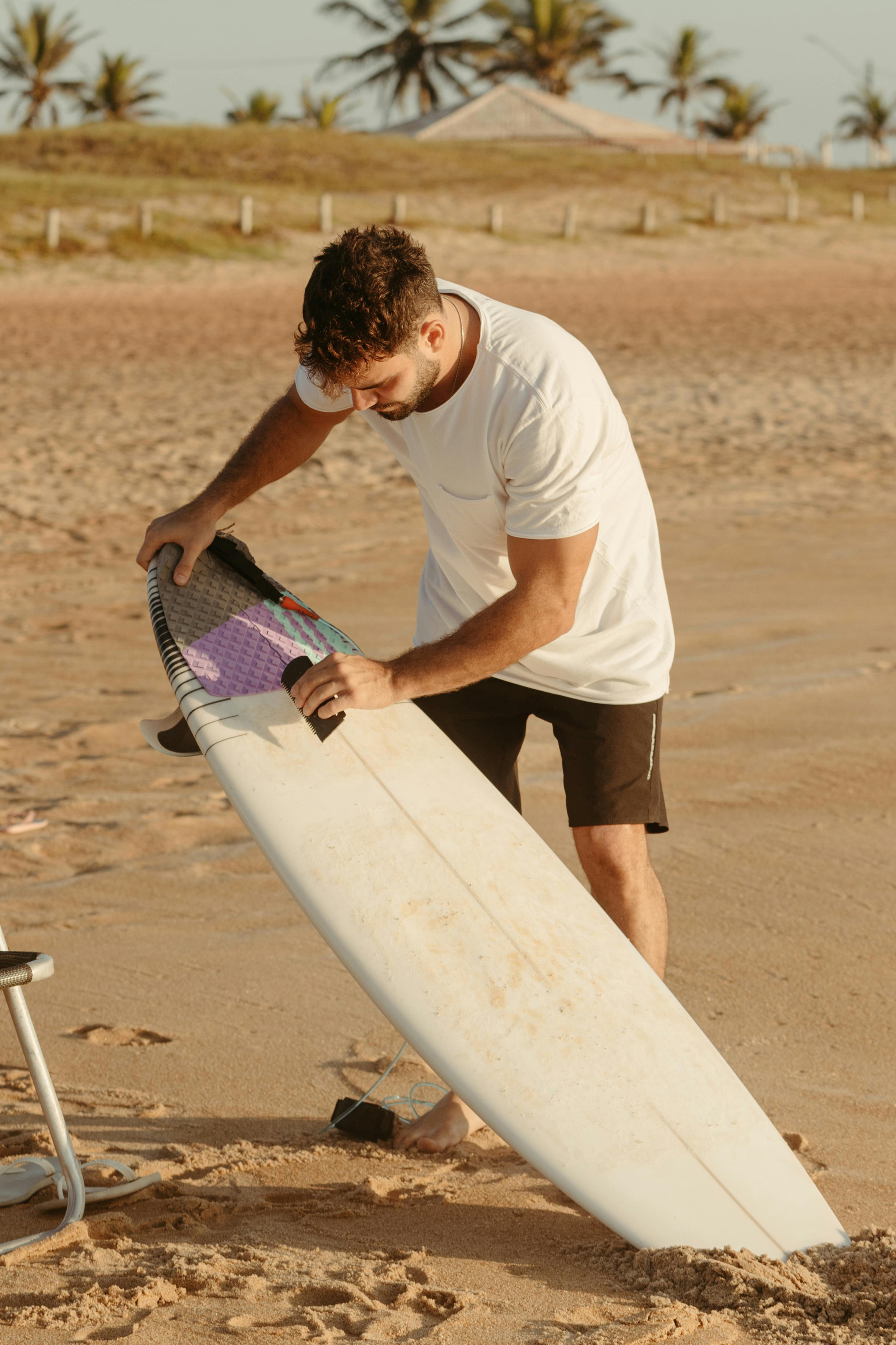 Man Sanding his Surfboard on Beach · Free Stock Photo