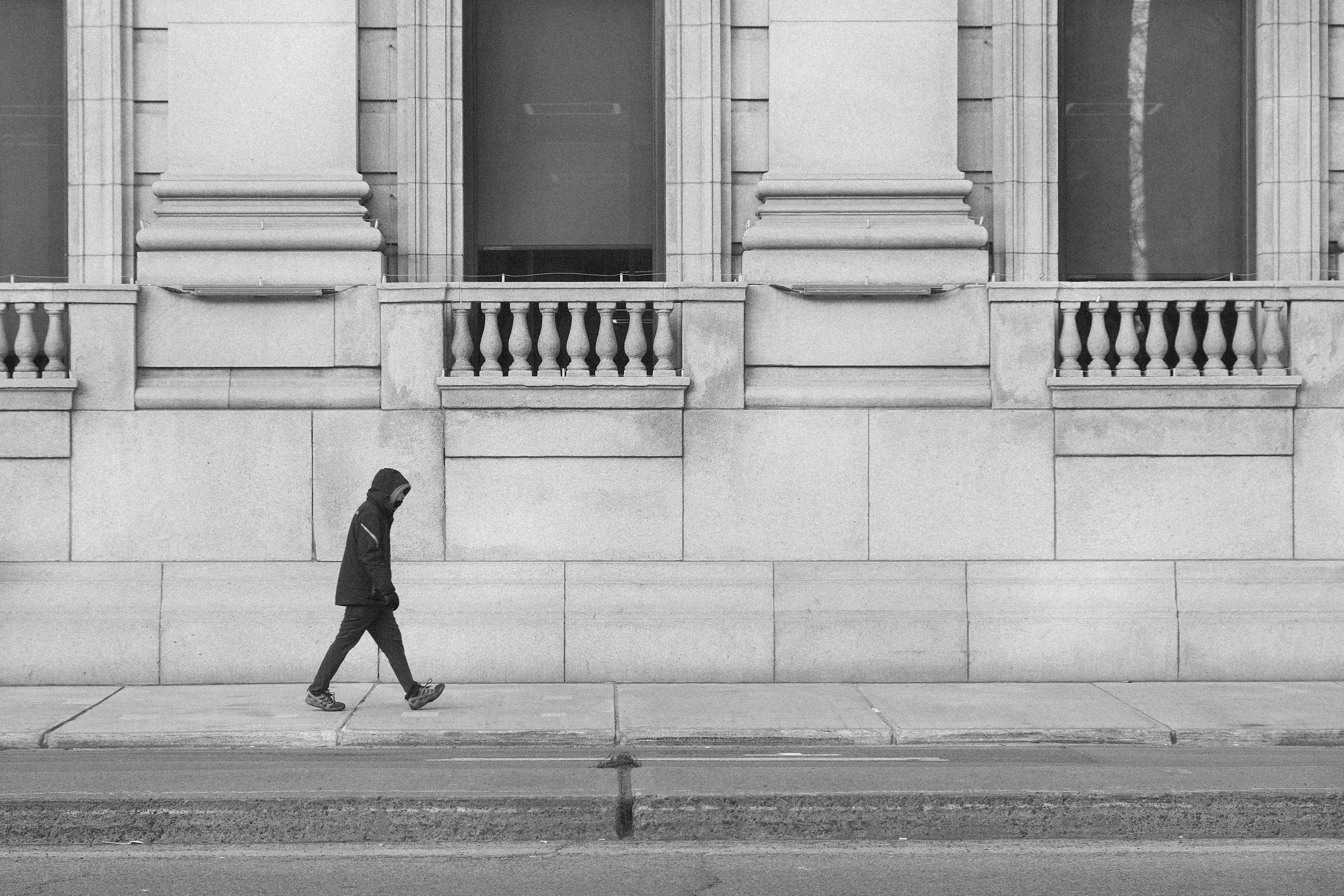 Hooded Passerby Walking Along the Sidewalk · Free Stock Photo