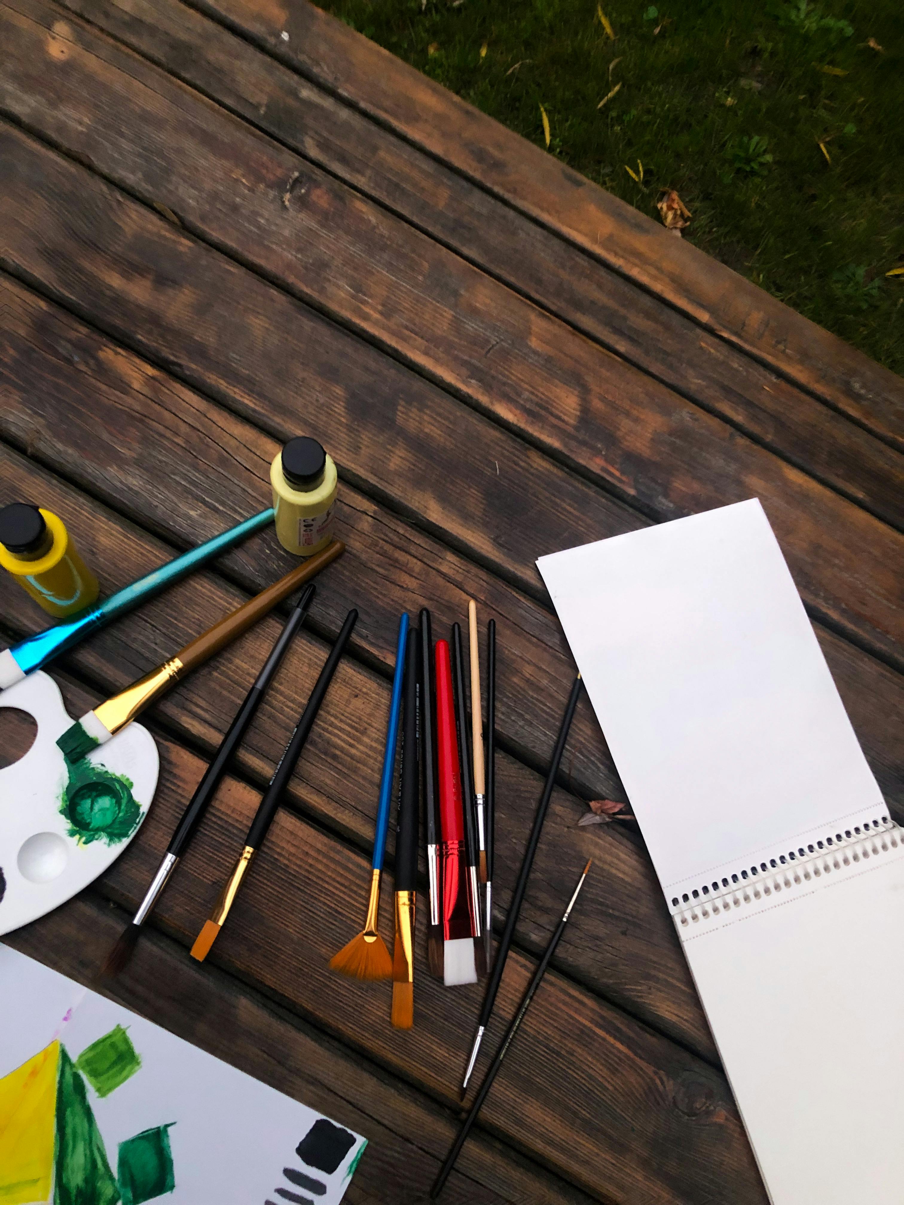 Paint Brushes and a Sketch Book Lying on a Bench · Free Stock Photo
