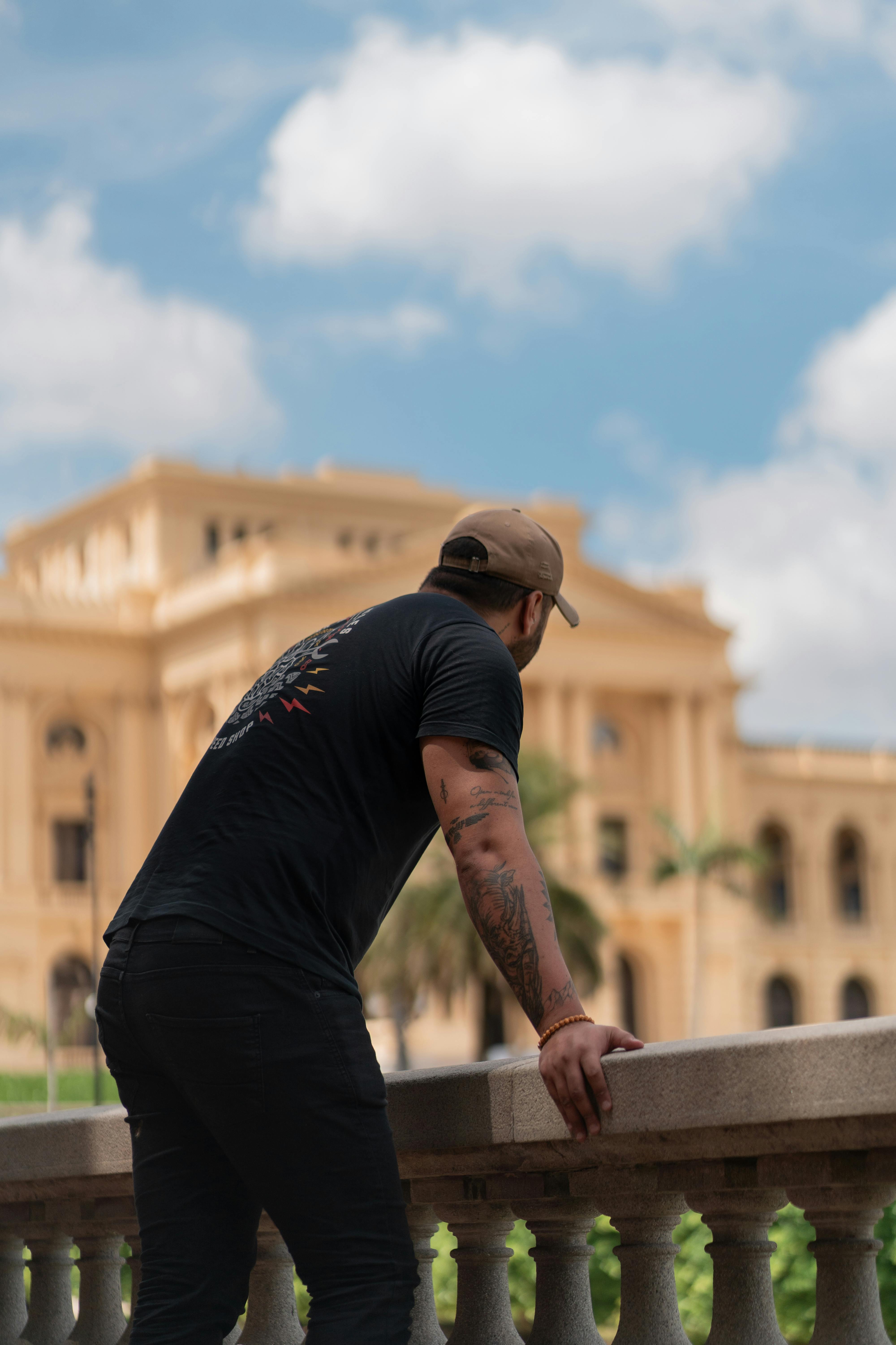 A Tattooed Man Standing against a Balustrade and Looking Toward a ...