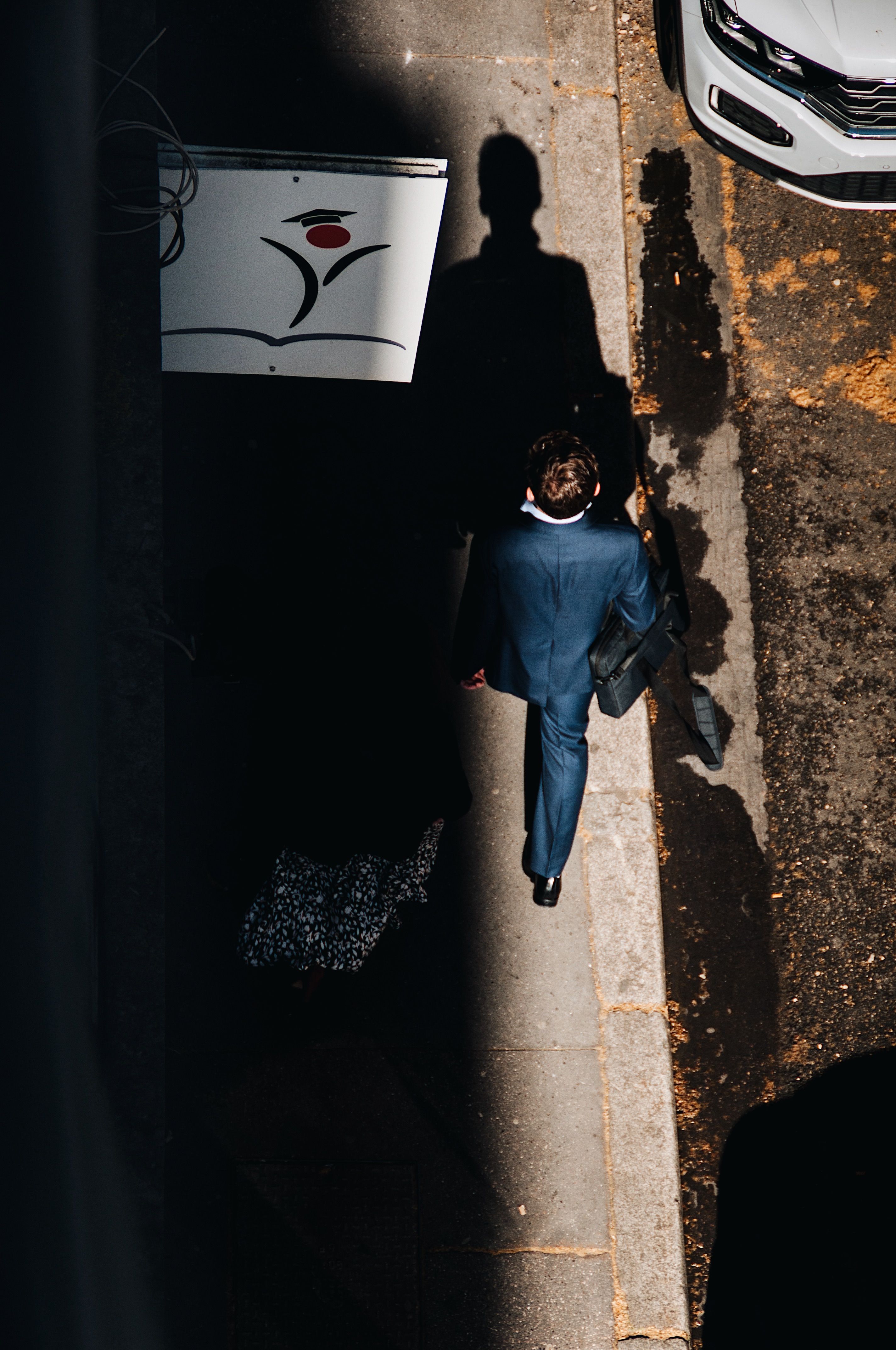 Back of a Person Walking along a Shaded Sidewalk · Free Stock Photo