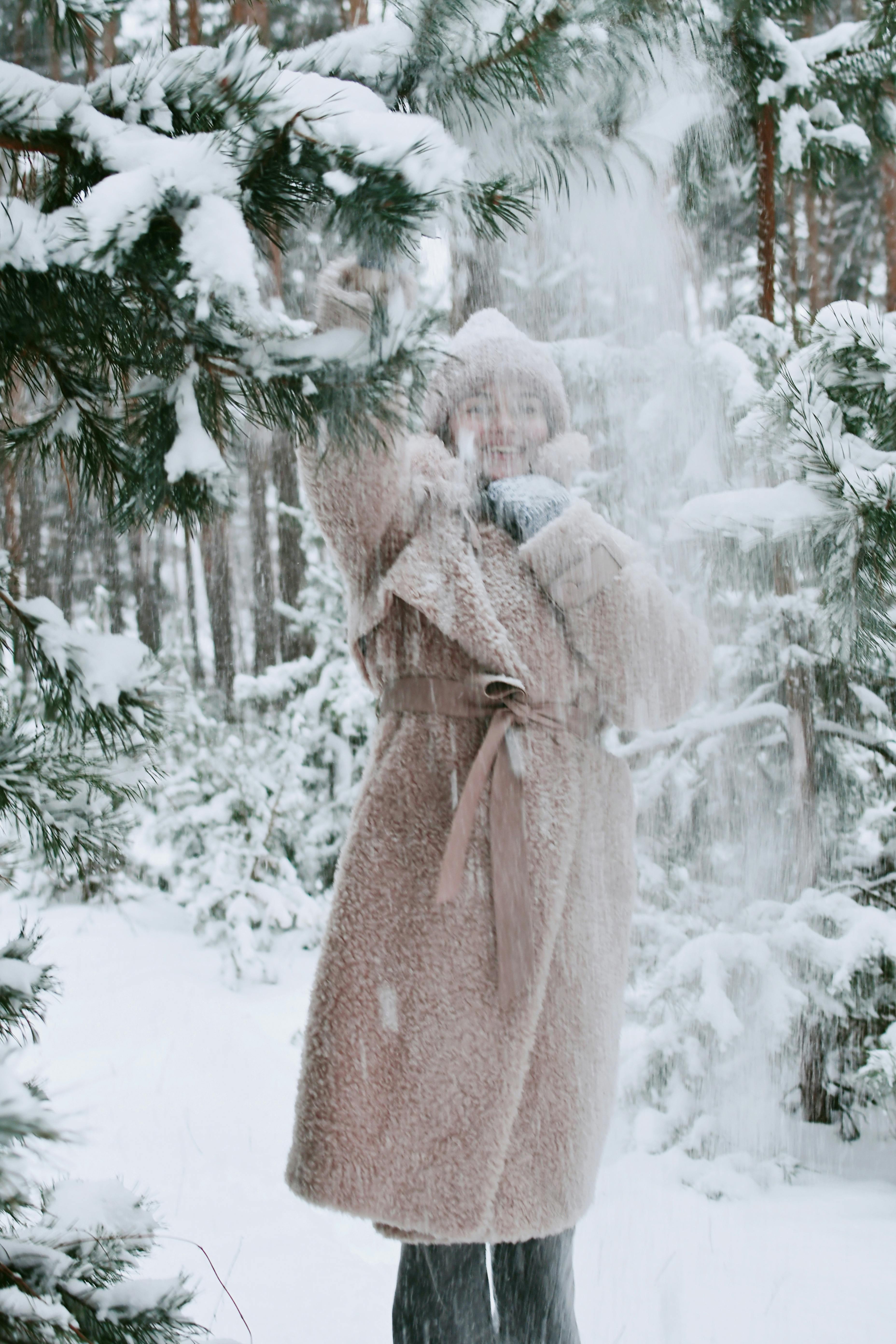 Woman in Faux Fur Knocking Snow Off a Branch on Herself · Free Stock Photo