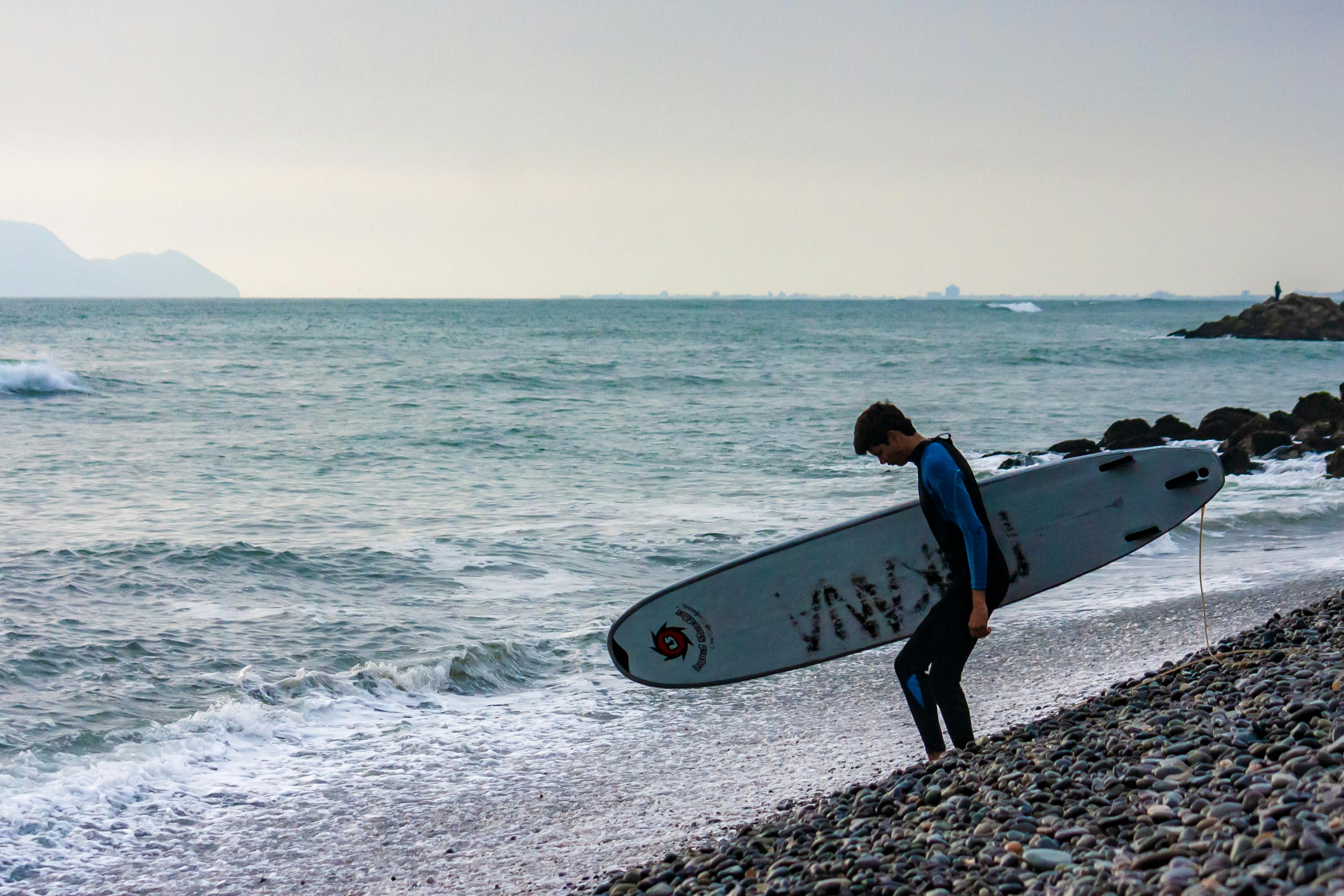 Man with Surfboard on Rocky Beach · Free Stock Photo